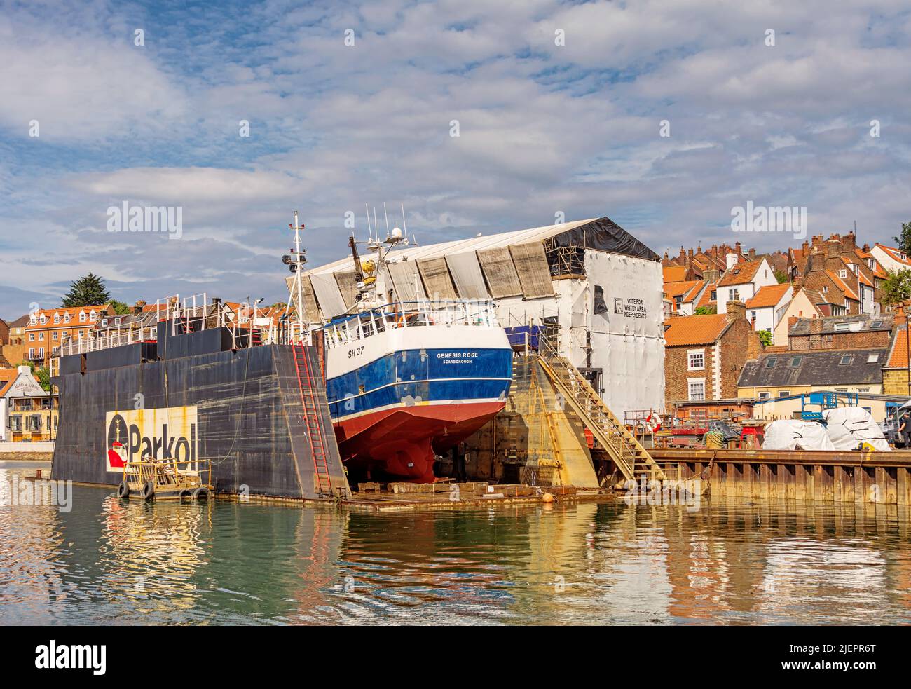 A dry dock beside a quay with a fishing trawler inside. Houses on are ...