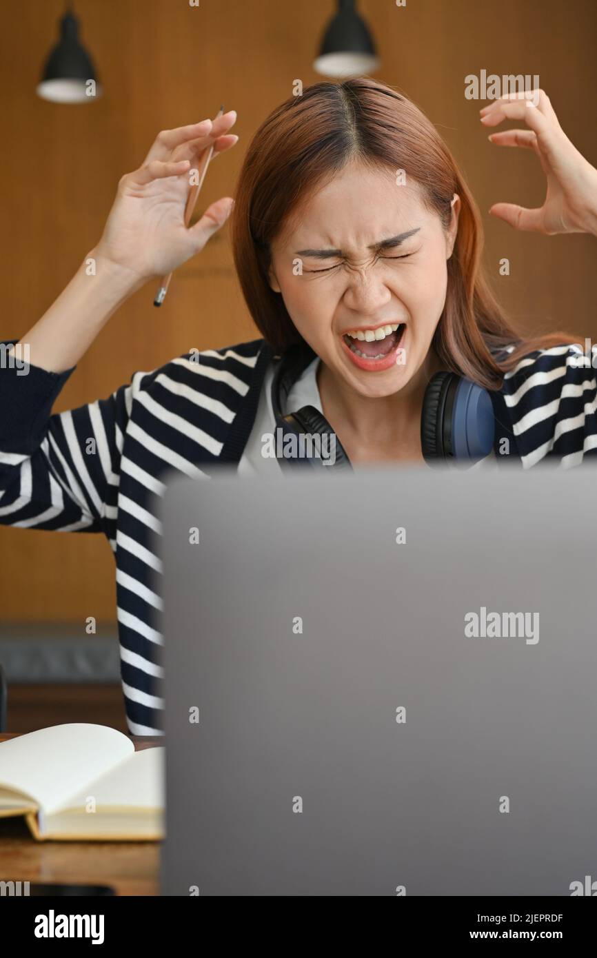 Furious and frustrated young Asian businesswoman sitting at her office ...