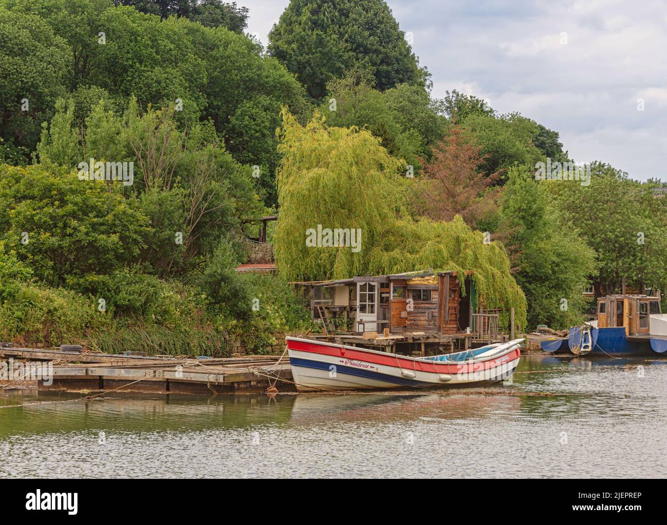 A rowing boat is moored beside a makeshift wooden cabin. Trees are ...