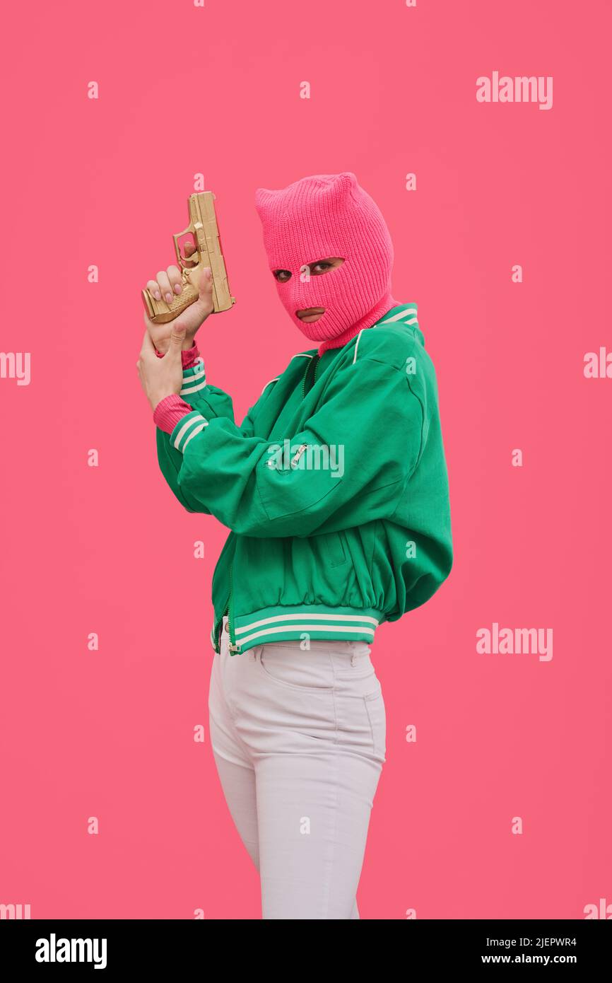 Portrait of criminal woman in jacket and balaclava in her face raising ...