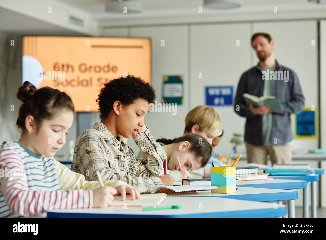 Side view at diverse group of children sitting in row and taking test ...
