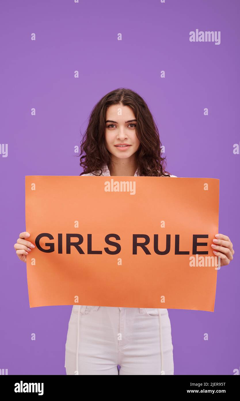 Portrait of young woman holding Girls Rule placard and looking at ...