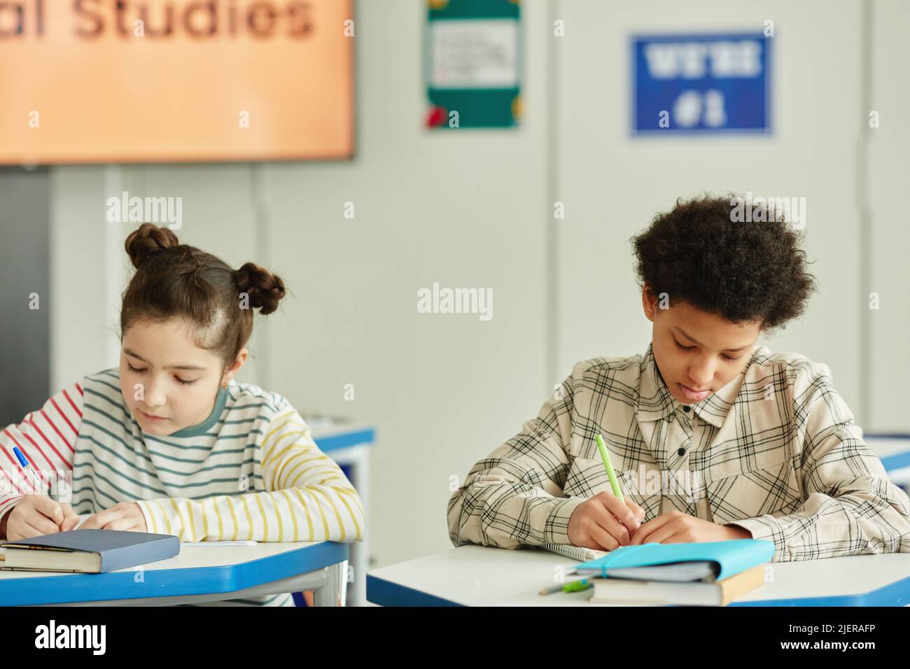 Front view at two children sitting at desk in classroom and writing in ...