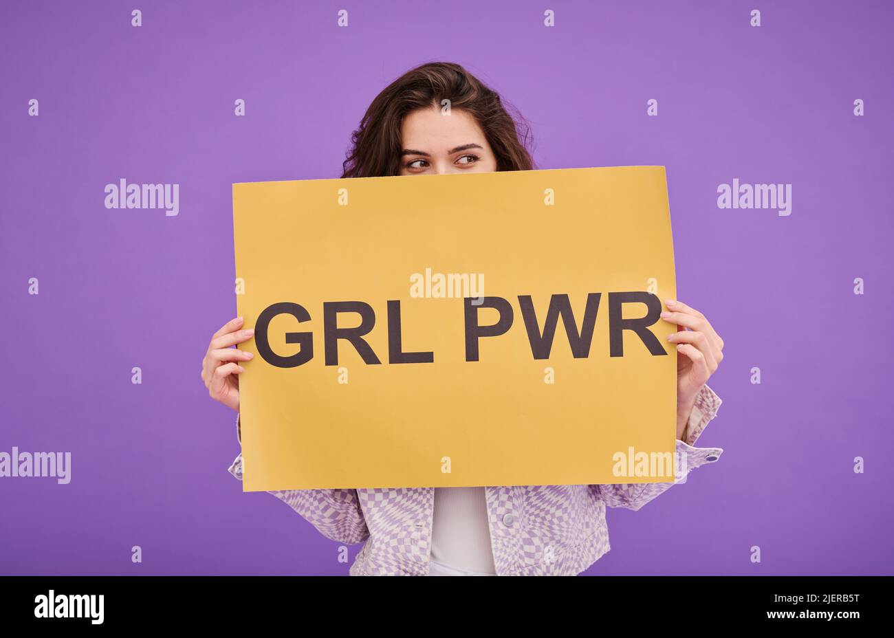 Portrait of young girl standing behind Girl Power poster against purple ...