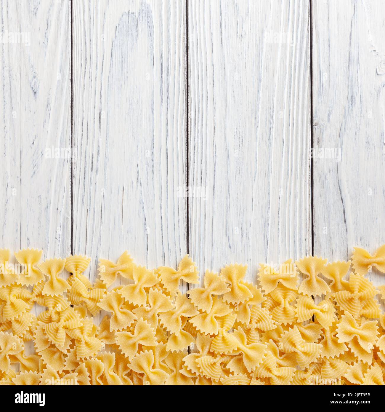 Uncooked farfalle rigate pasta on white wooden background with copy ...