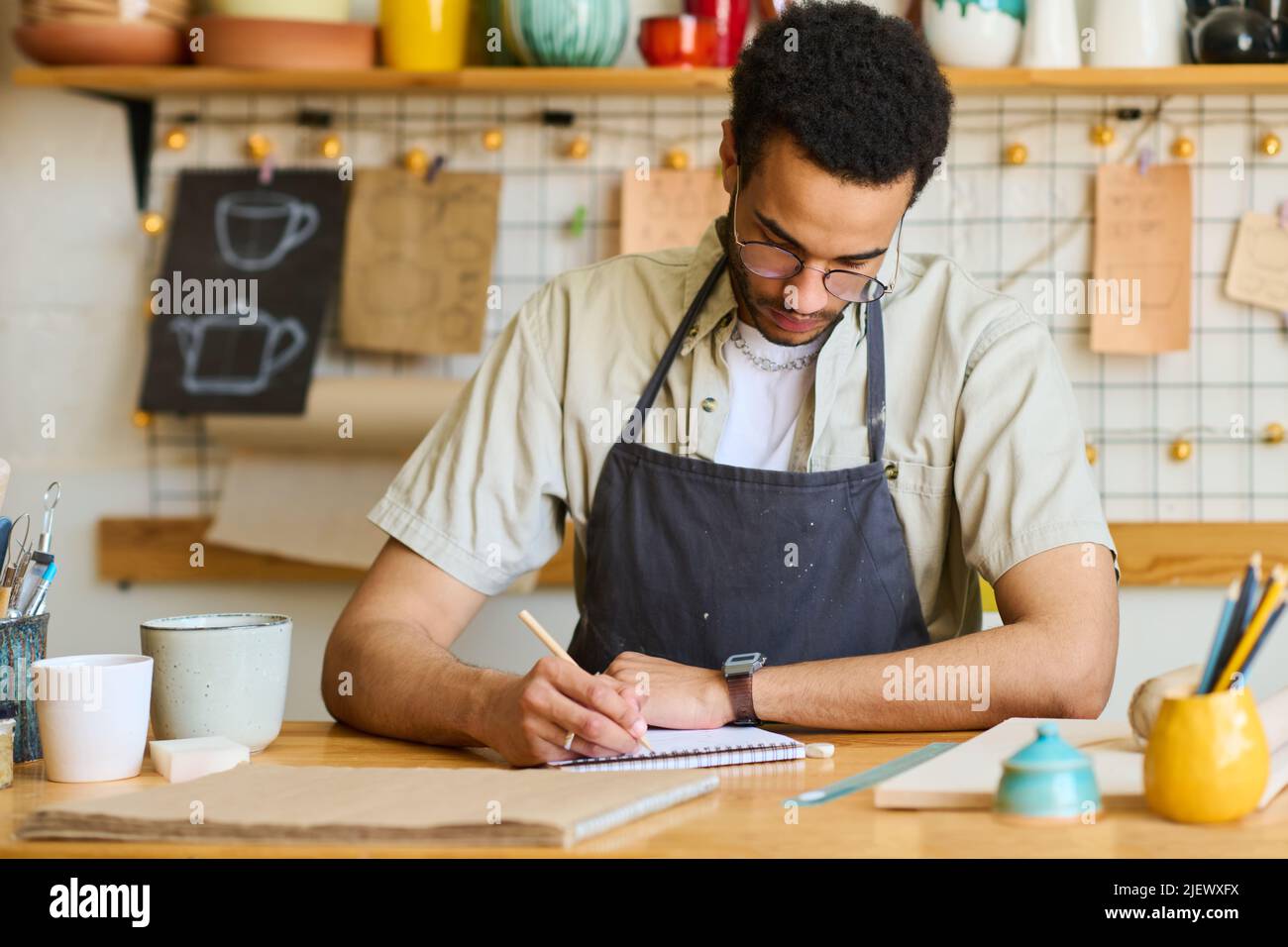 African American guy in apron making notes in notepad while sitting by ...