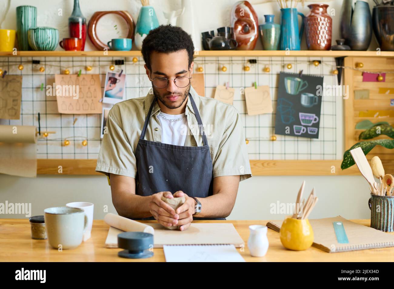Young creative black man skilled in making earthenware sitting by table ...