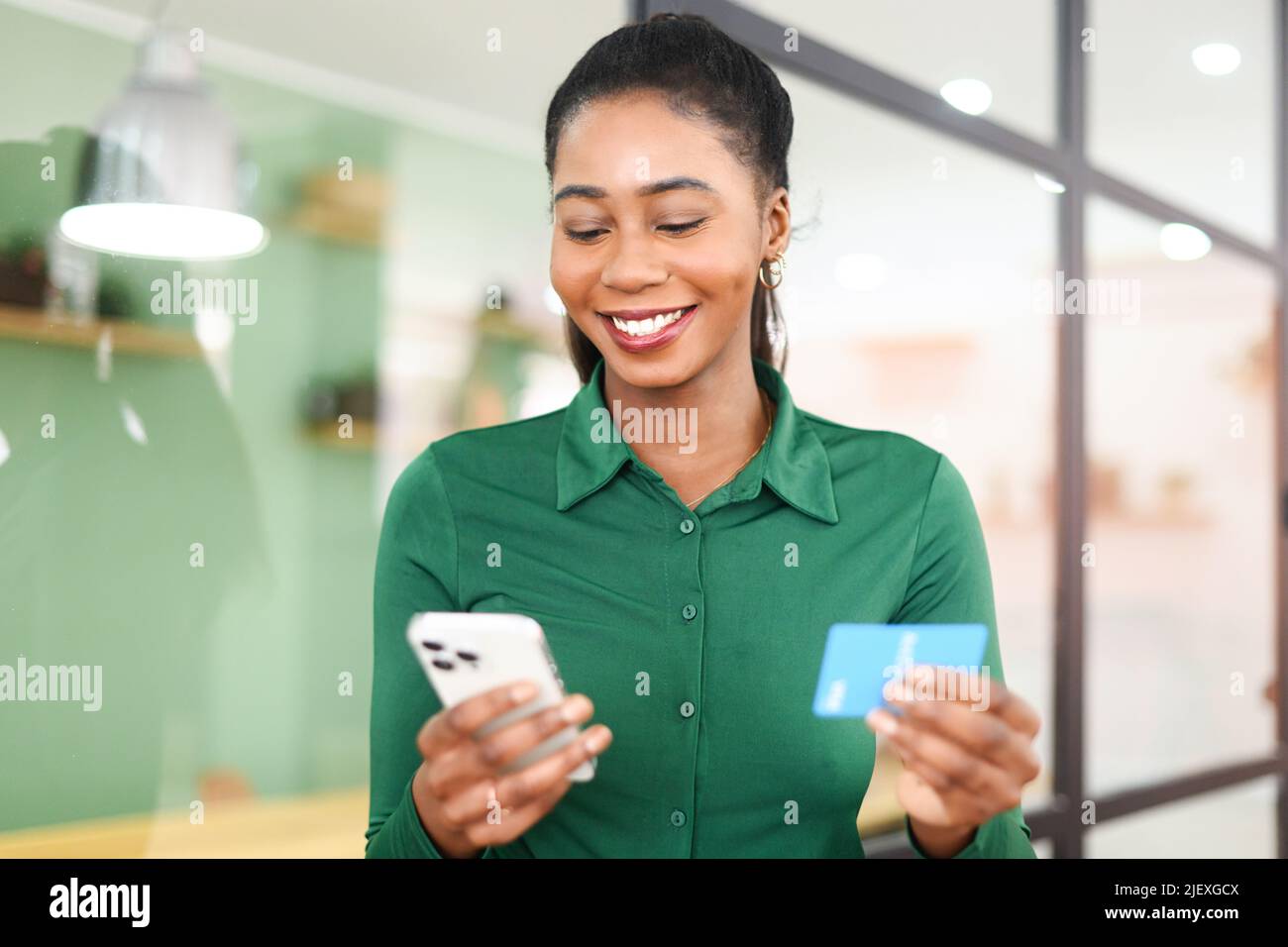 Cheerful african-american young woman holding smartphone and credit ...