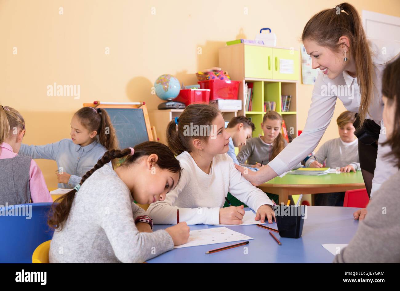 Group of school kids with pens and notebooks studying in classroom with ...