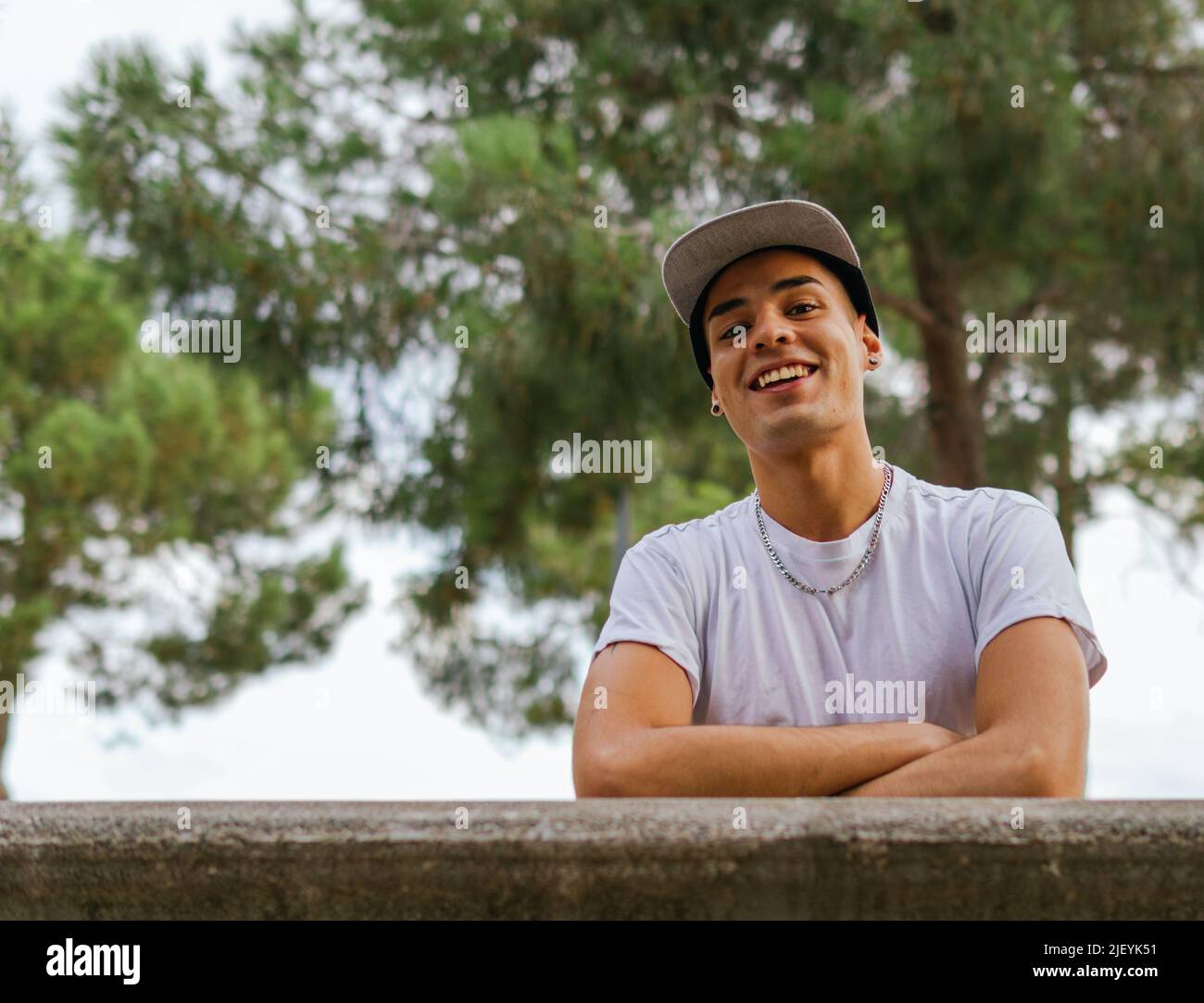 Low angle shot of a smiling guy with cap and arms grossed looking down ...