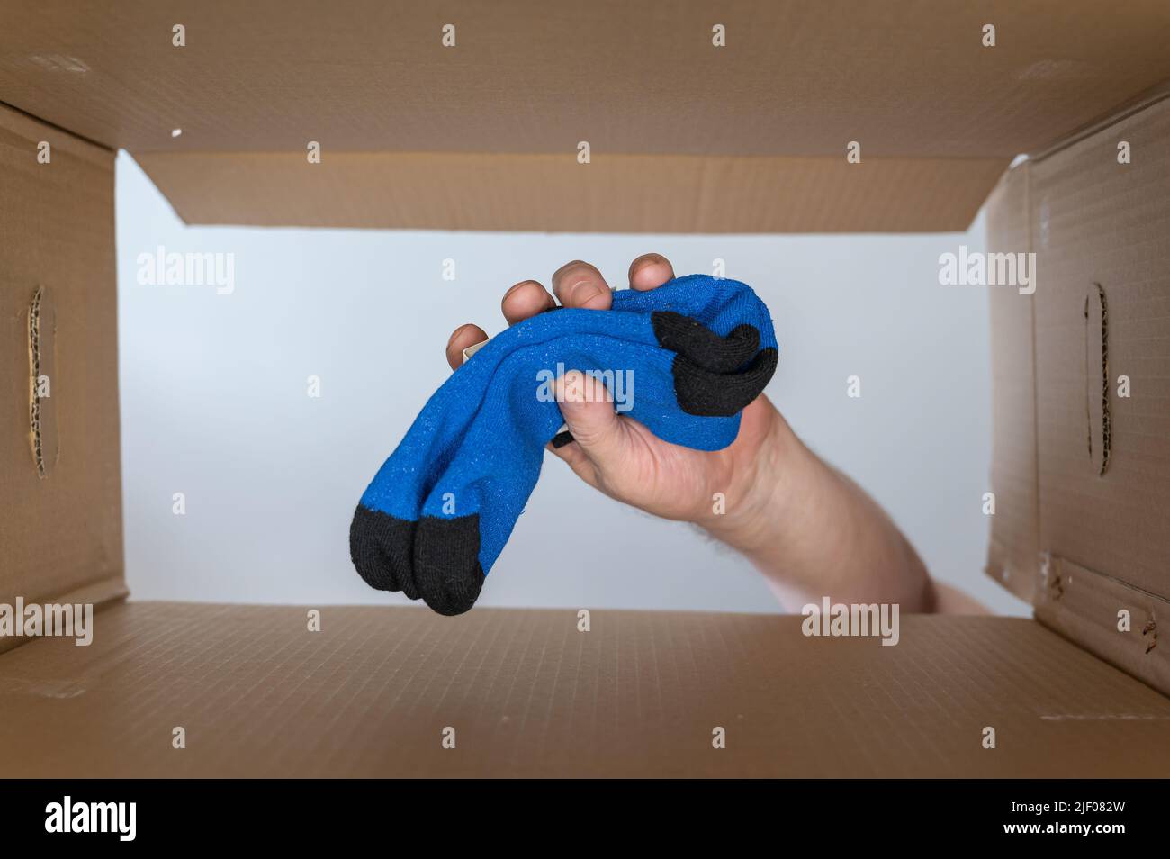 A man's hand puts his socks in a cardboard moving box. Folded blue and ...