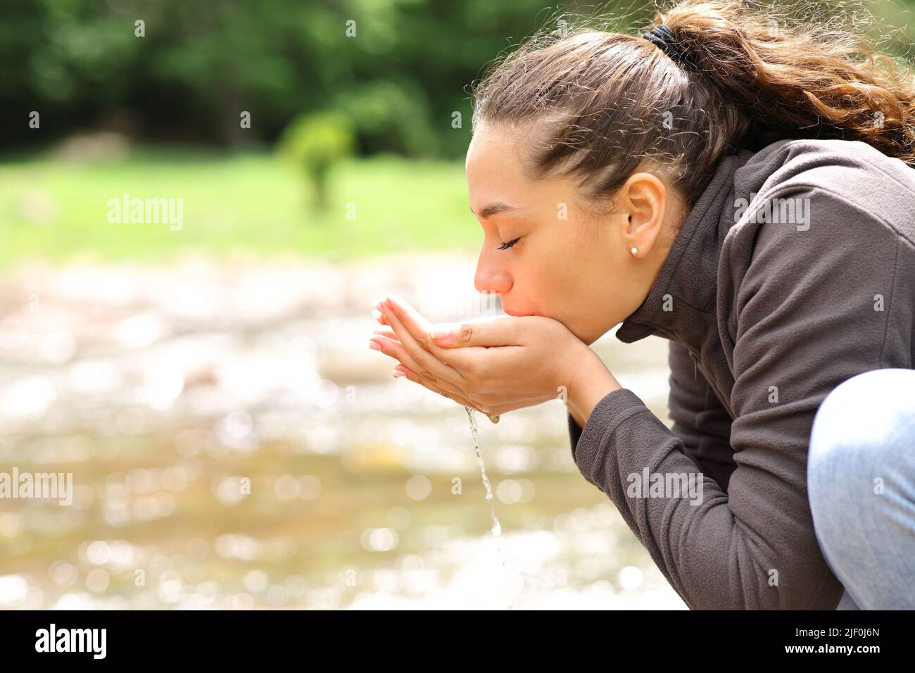 Side view portrait of a woman drinking water from river in the mountain ...