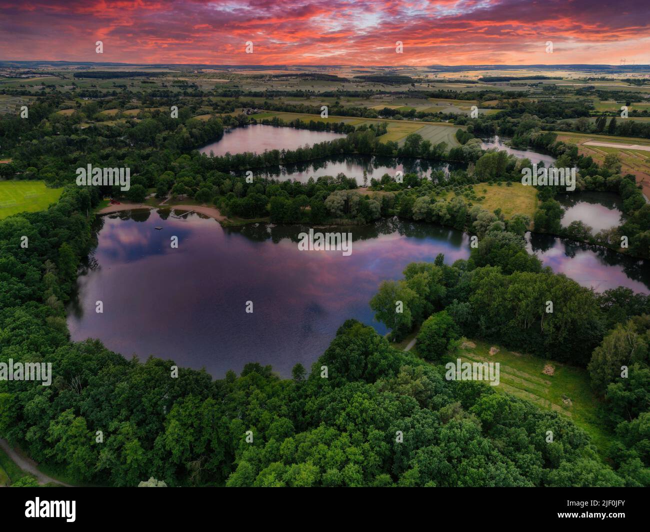 The small lakes surrounded by green trees under a cloudy sky at sunset ...