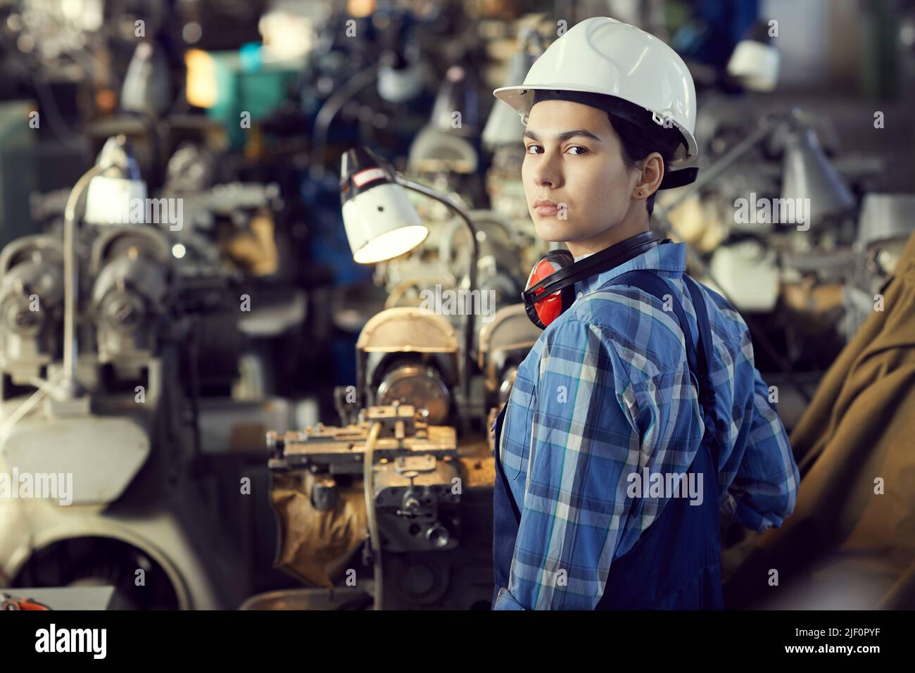 Portrait of serious young female production worker in hardhat standing ...