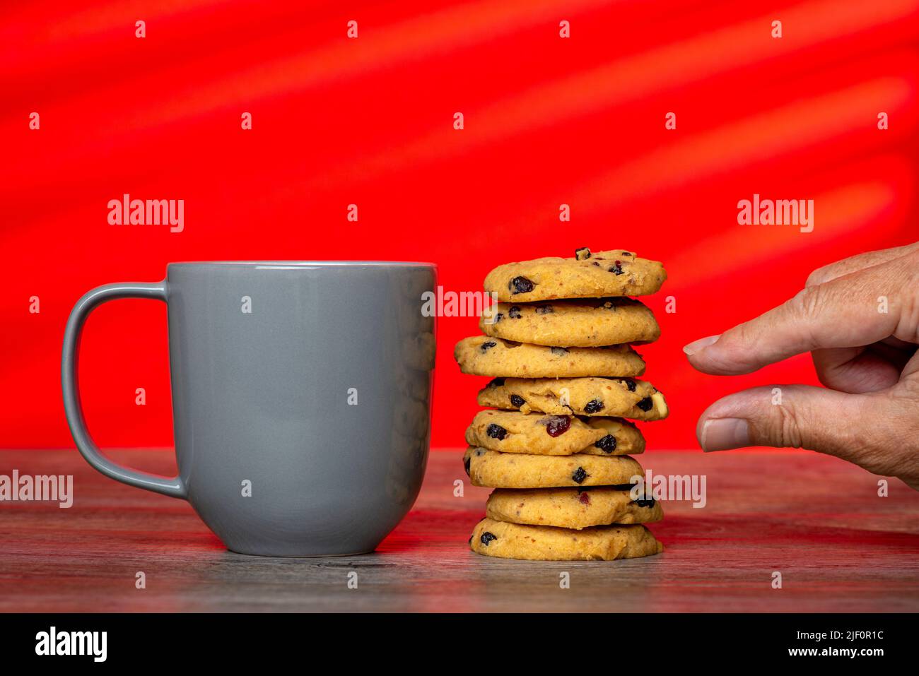 stack of home cooked cookies and a grey mug against a red background ...