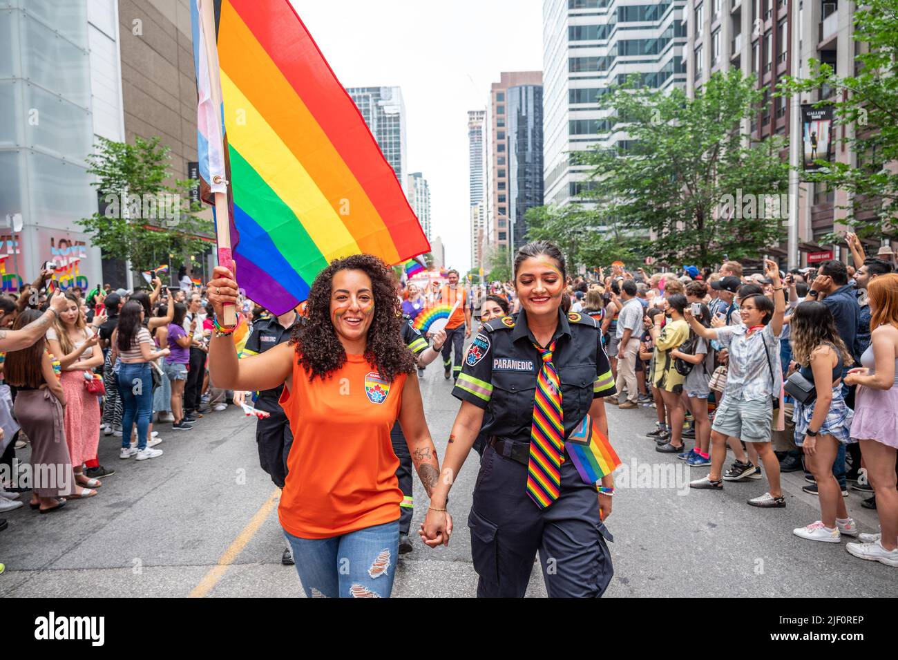 Two female people holding hands and holding the Progressive Pride Flag ...