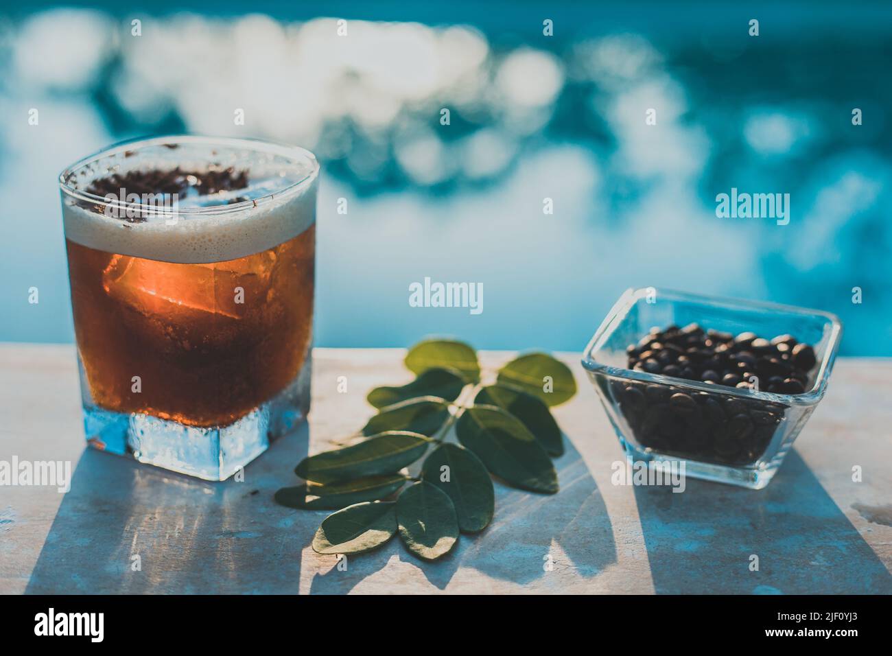Fresh iced coffee cocktail with coffee beans and blue swimming pool in ...