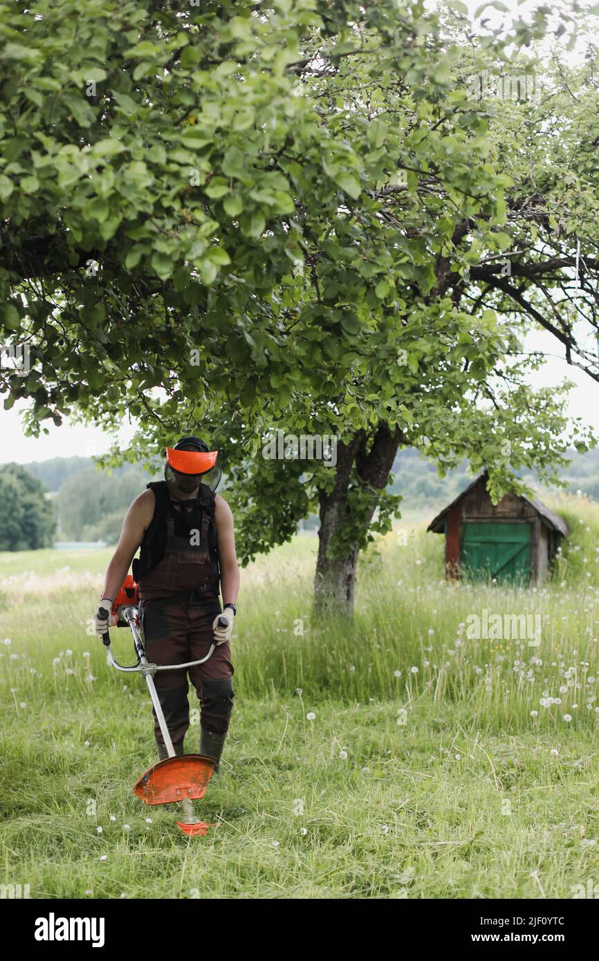 Man mowing tall grass with petrol lawn trimmer in the garden or ...