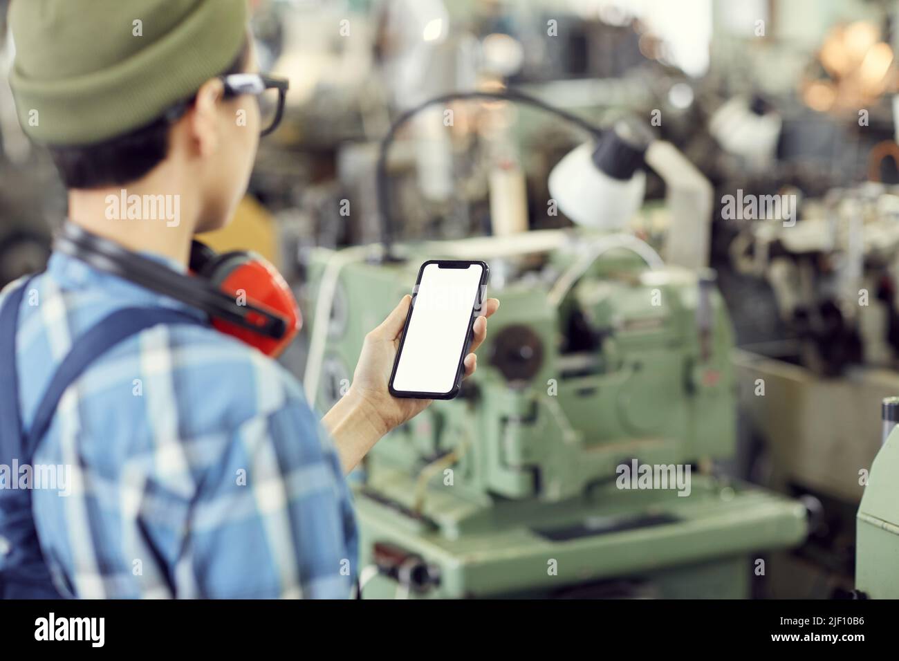 Rear view of hipster machine operator standing at factory and ...