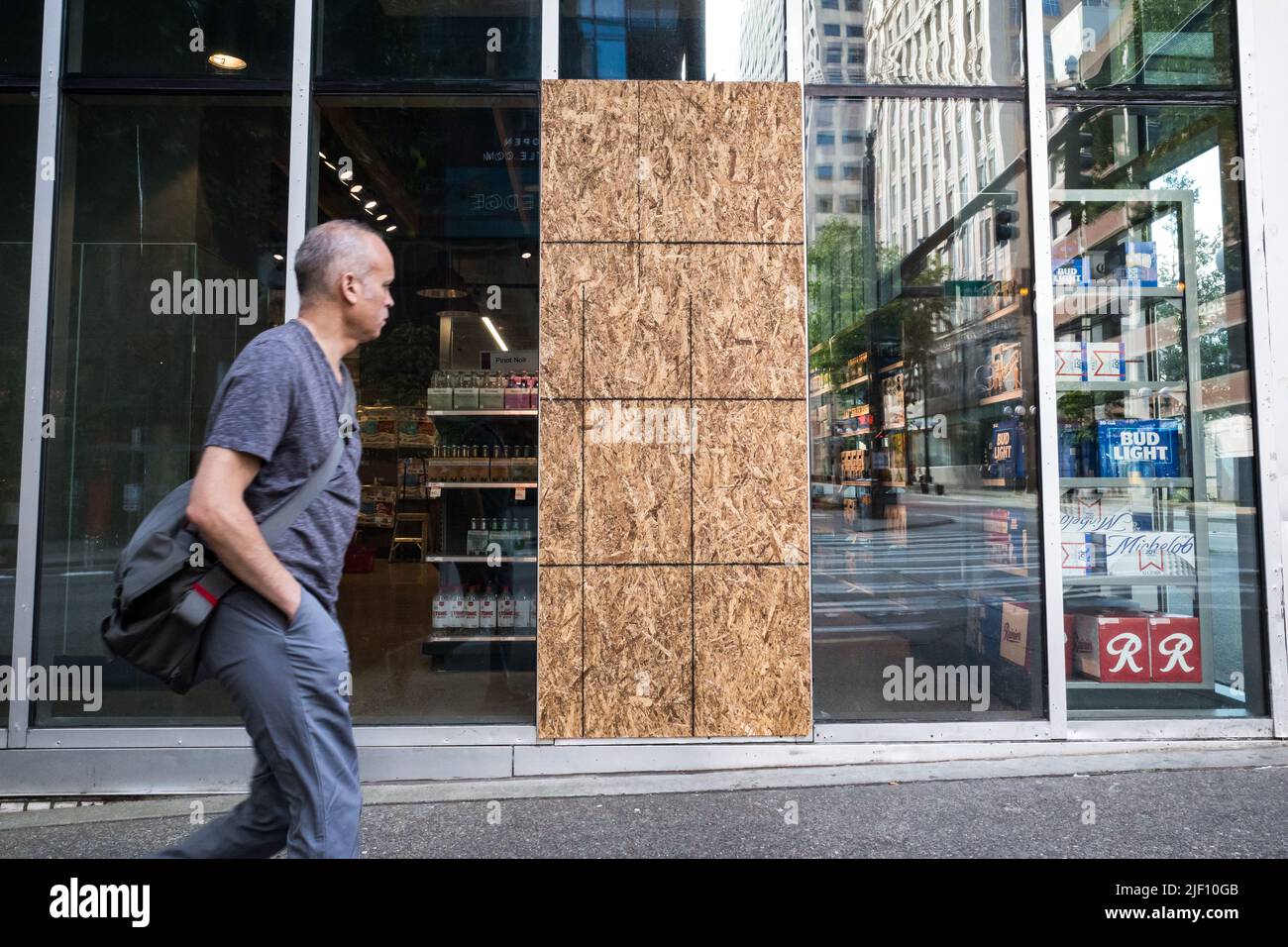 Seattle, USA. 28th Jun, 2022. A person passing a boarded up smashed ...