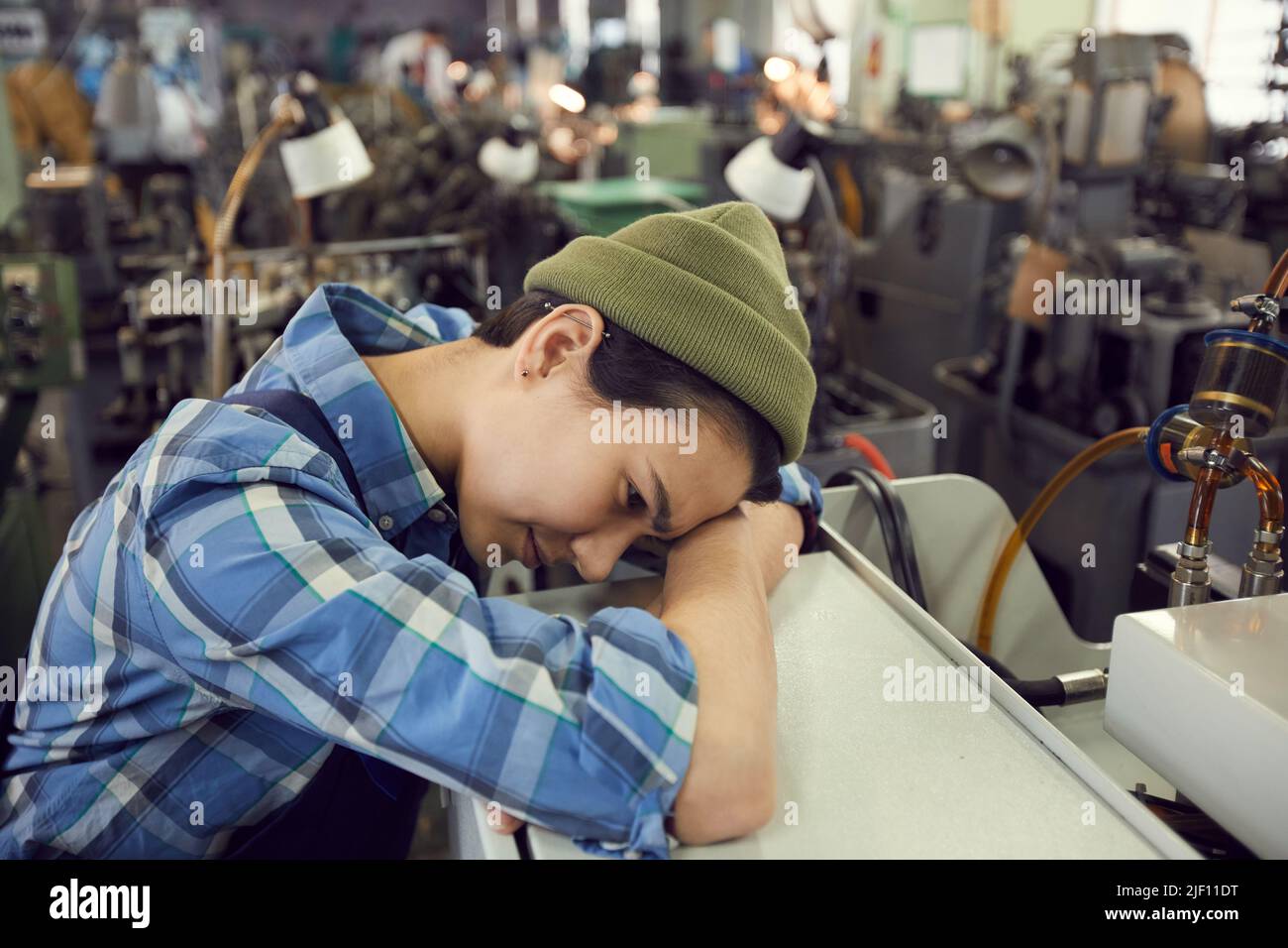 Fatigued young female production worker in green hat tired from work ...