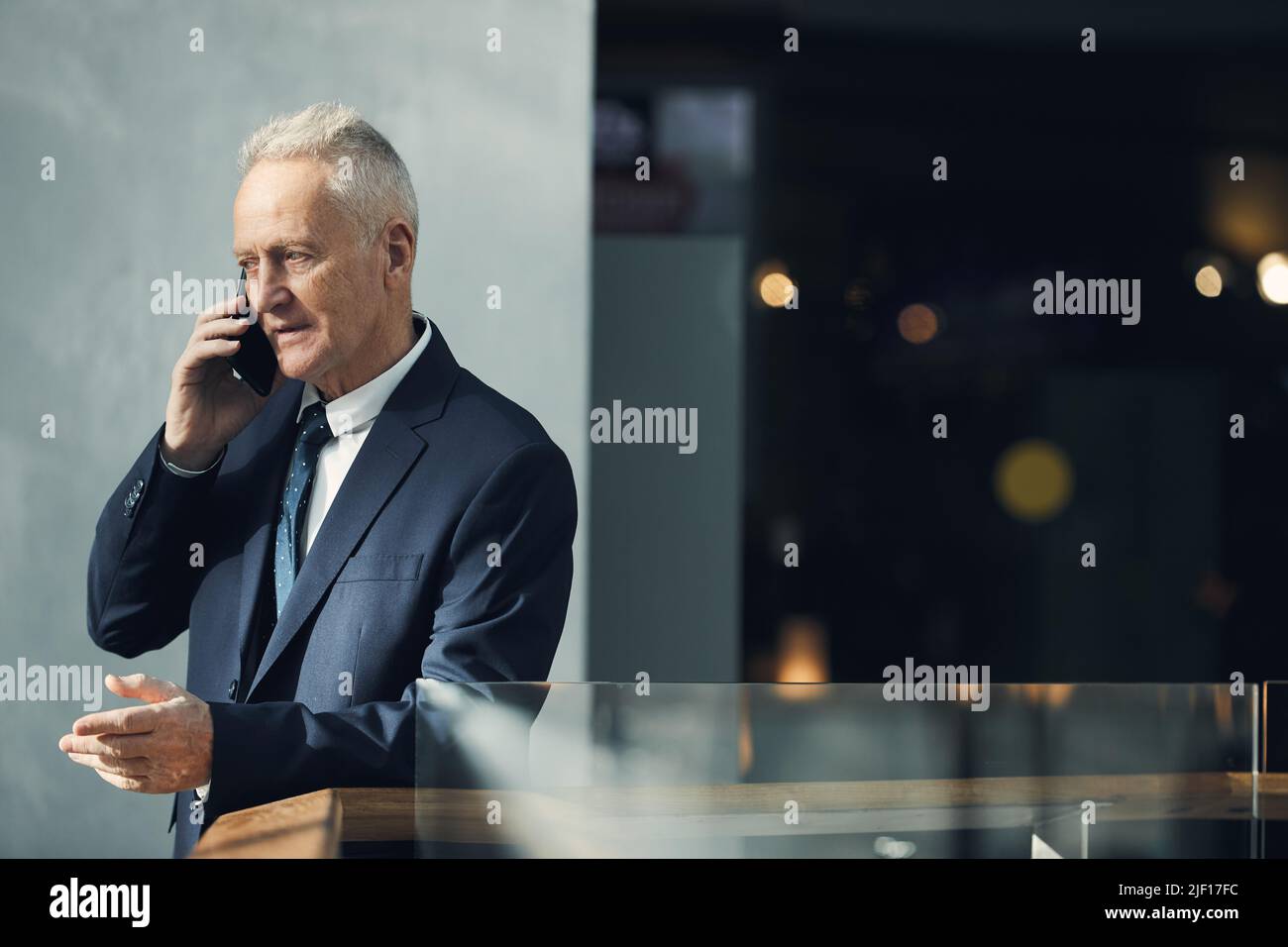 Concerned senior business manager in suit leaning on railing in hall ...
