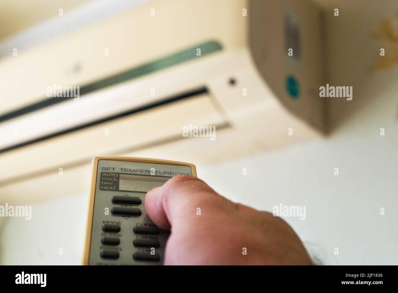 A man turns on the air conditioner with a remote control in a hot ...