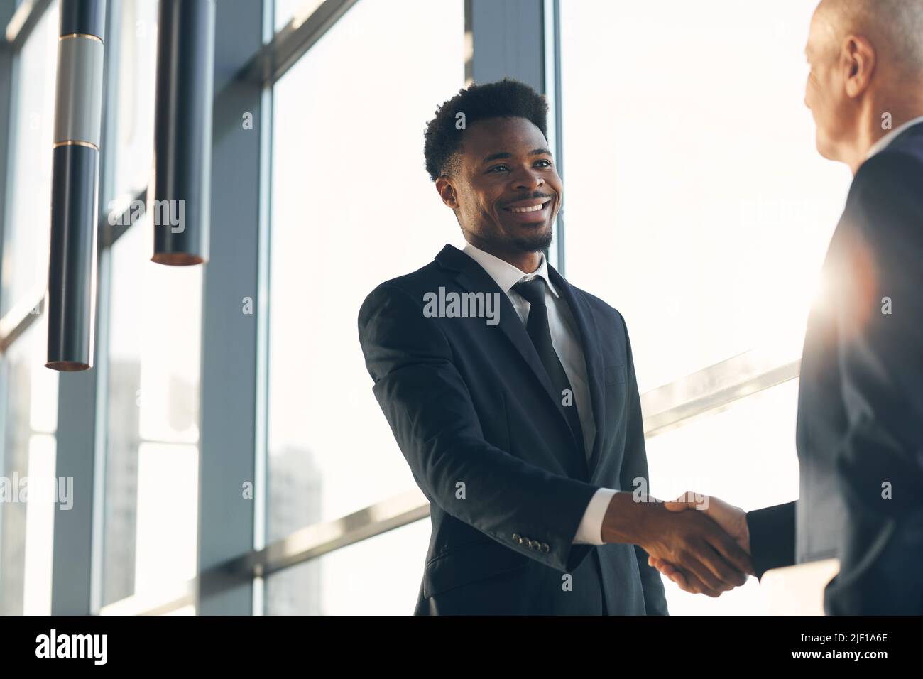 Cheerful Handsome Young Black Businessman In Suit Standing At Panoramic Window And Making