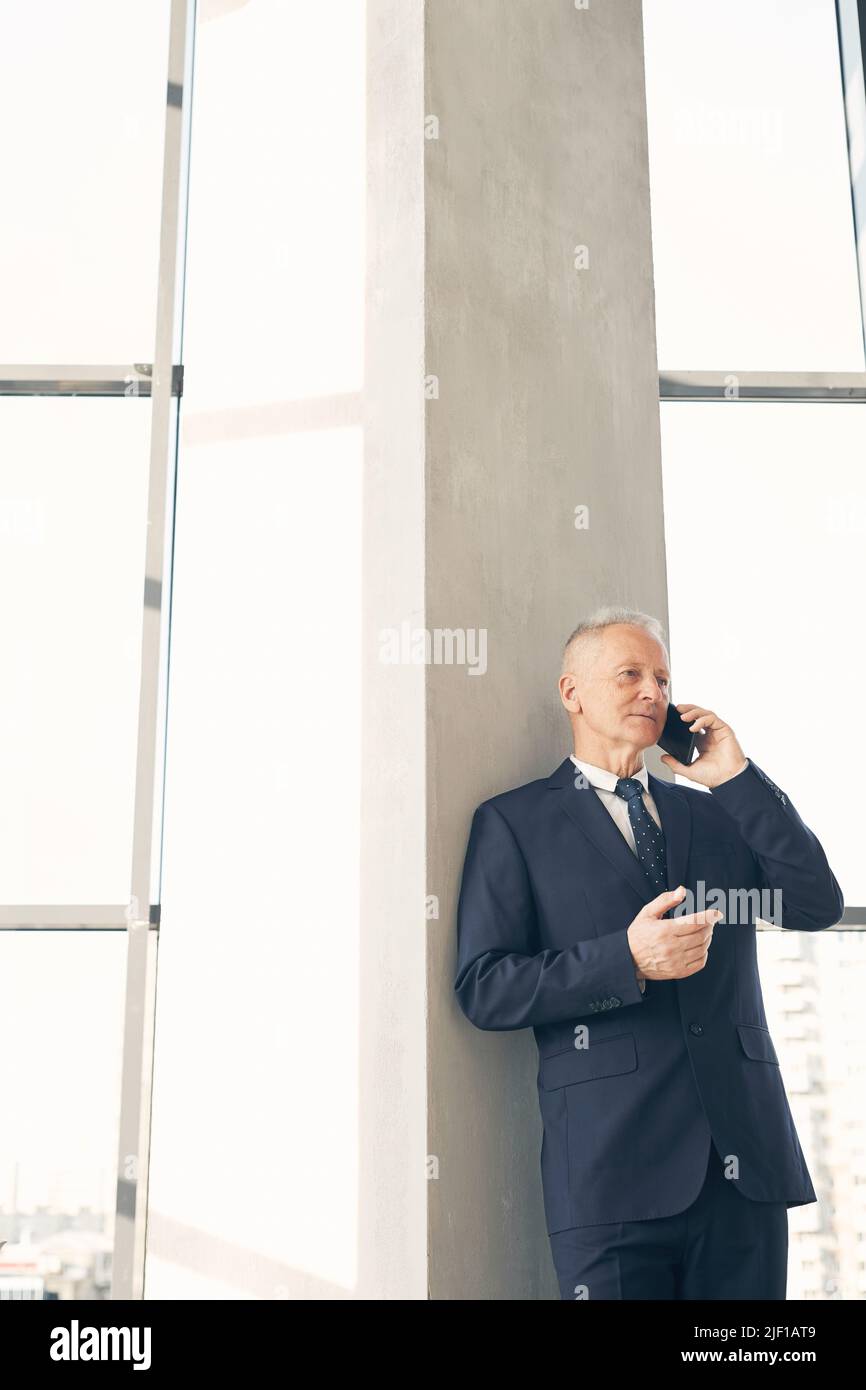 Content handsome mature businessman in formal suit leaning on column in ...