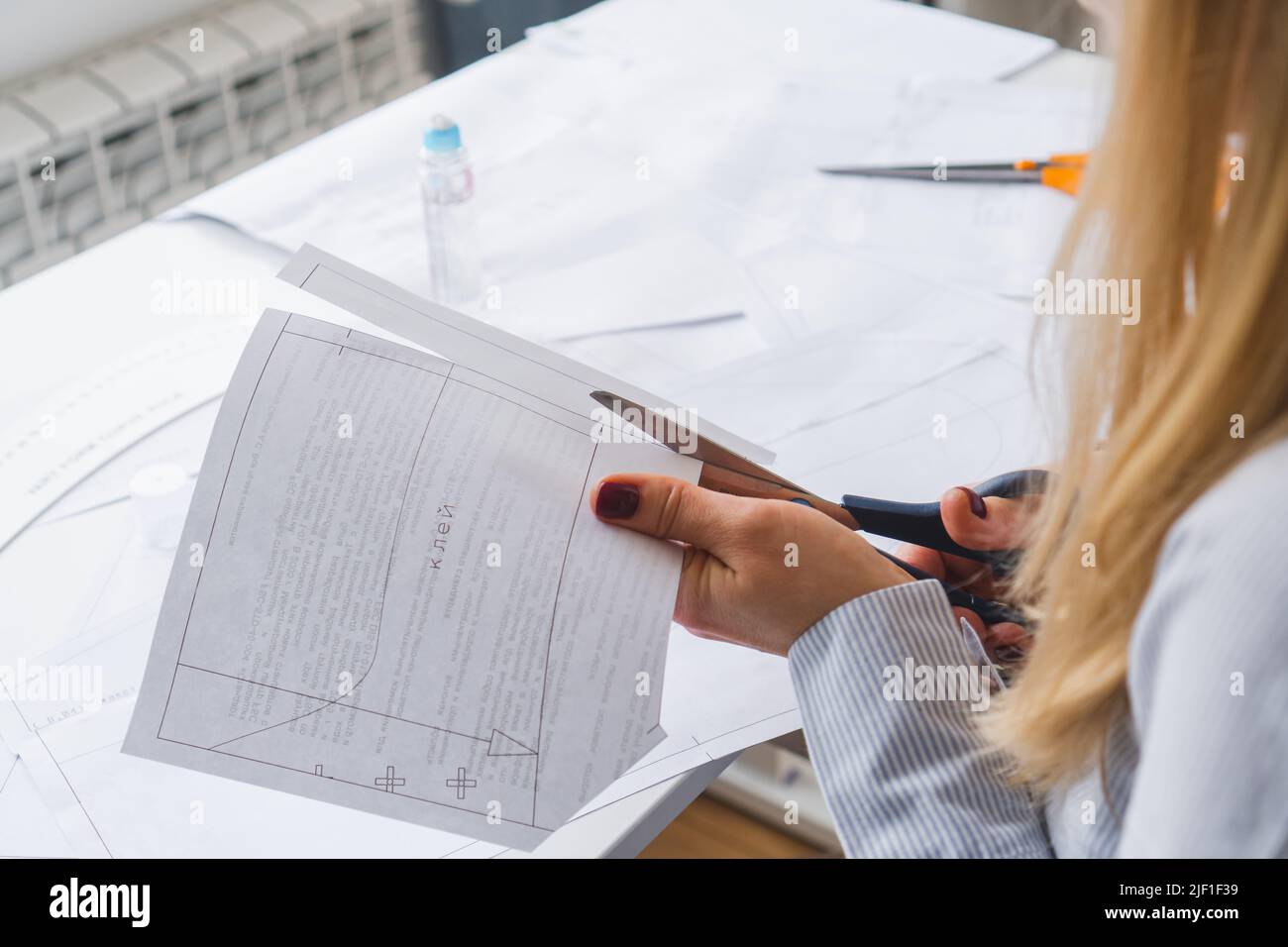 Seamstress cuts papper patterns for dress with scissors. Design ...