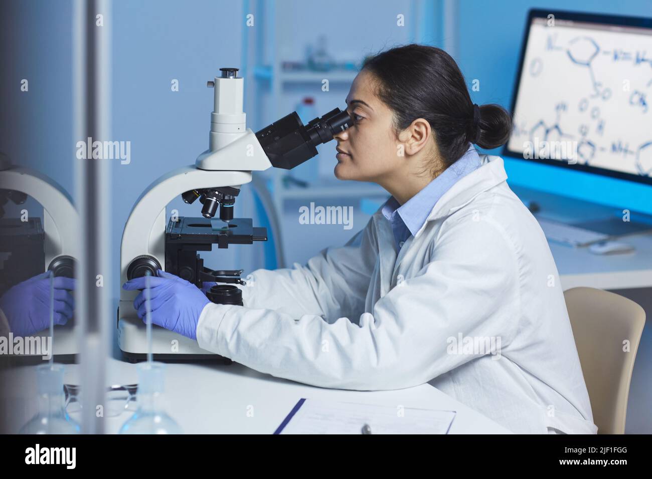 Serious concentrated young Indian chemical researcher in lab coat and ...