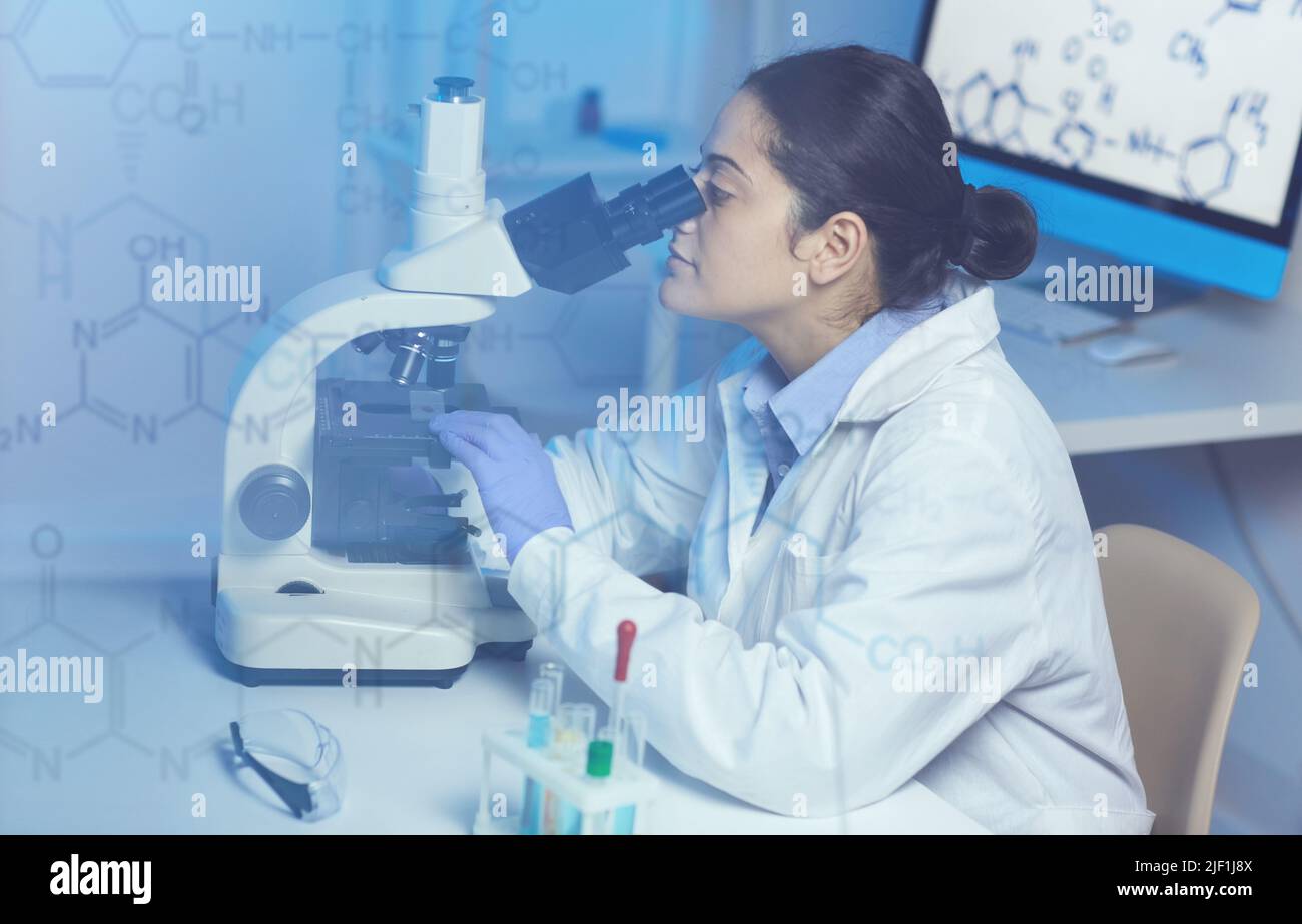 Serious young mixed race doctor of chemistry in lab coat sitting at ...