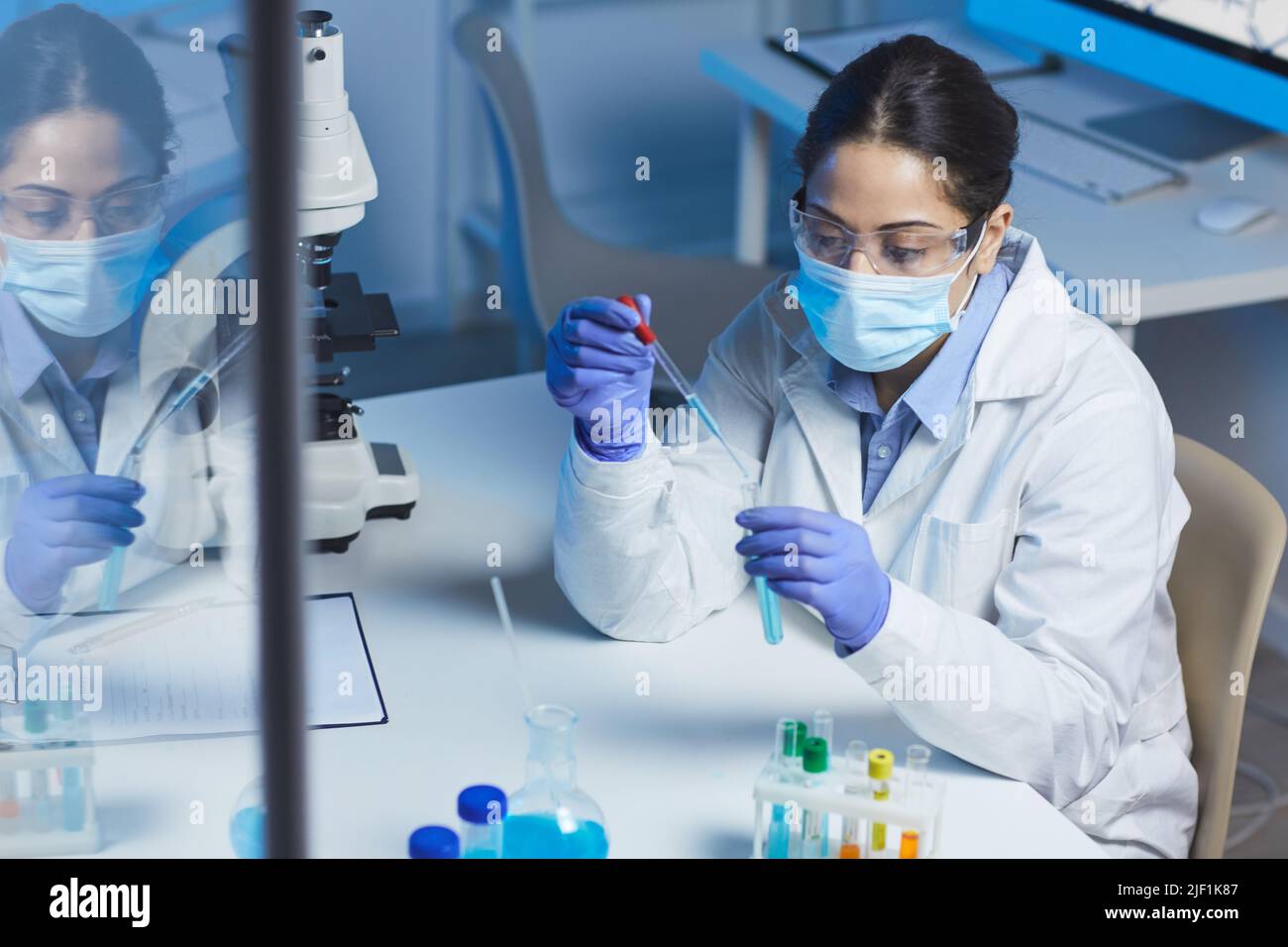 Serious young Indian female chemical researcher in protective workwear ...