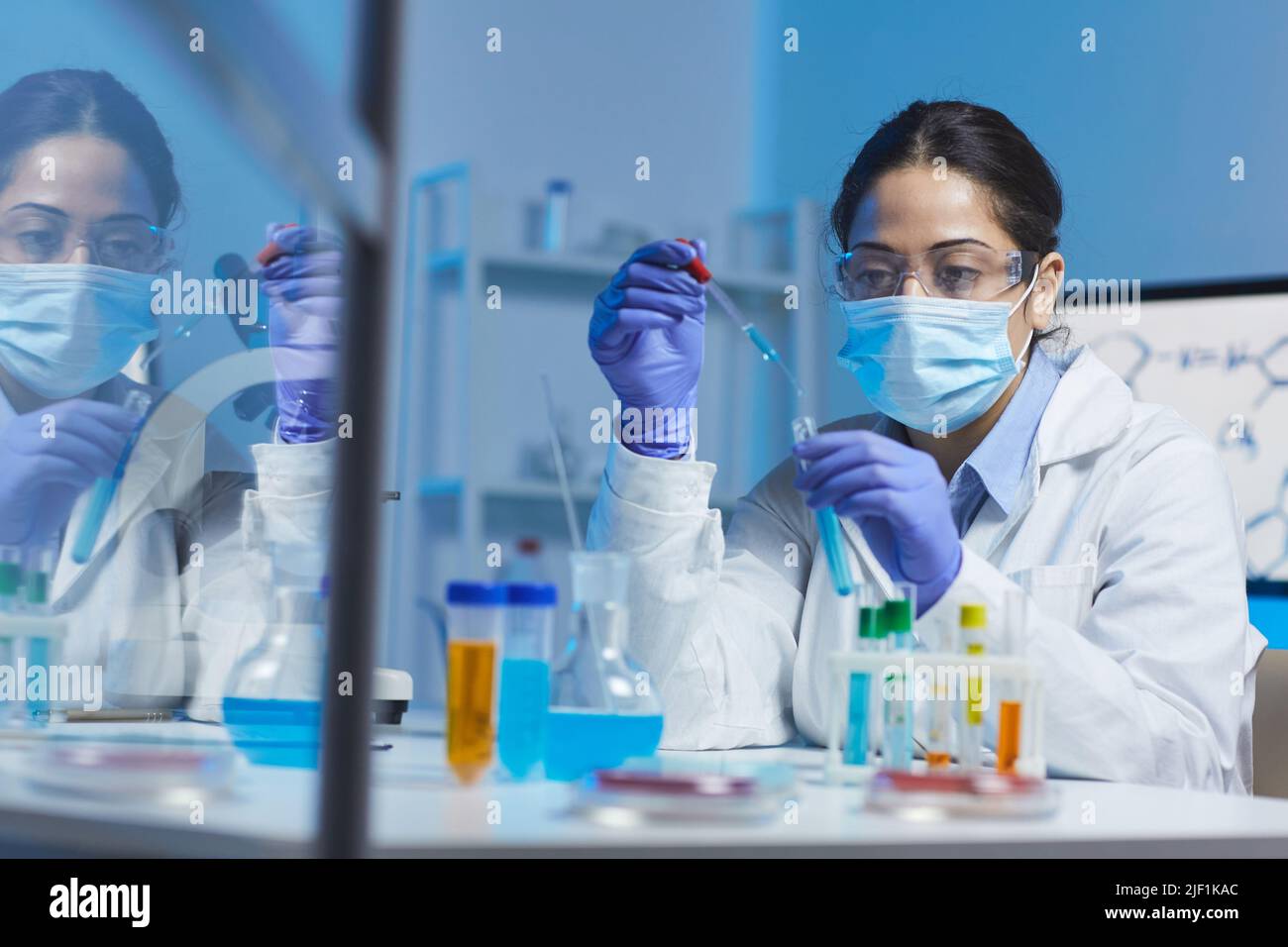 Concentrated young Indian female laboratory worker in mask and safety ...