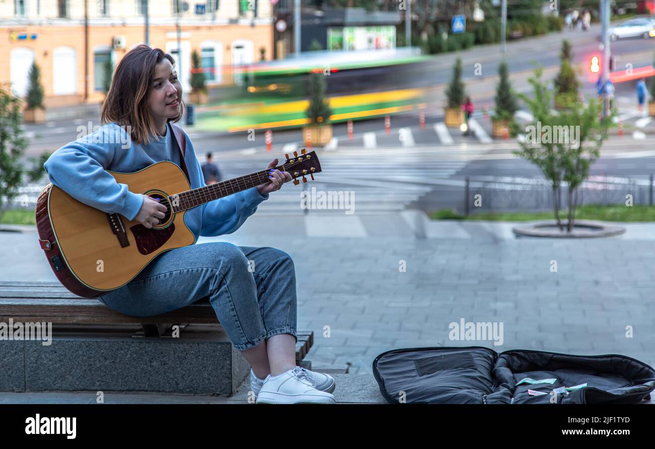 Female musician busking playing acoustic guitar and singing outdoors in ...