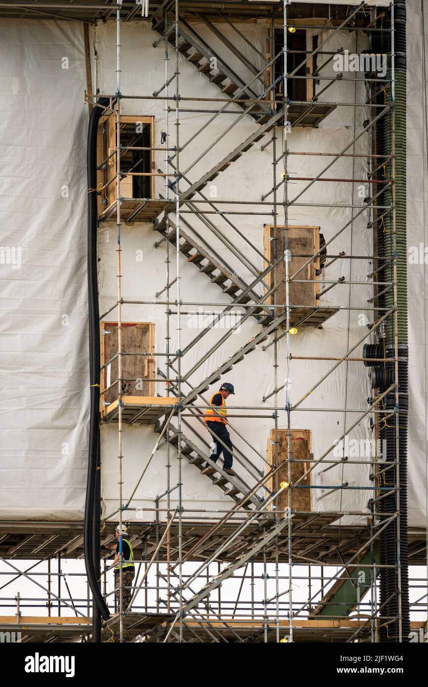 Two workers descend the stairs of a scaffold erected up the side of a ...