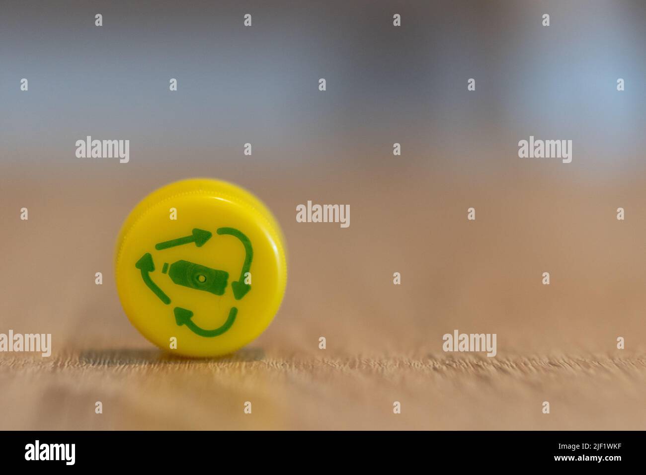 A green recycling logo on a plastic bottle cap with a blurry background ...