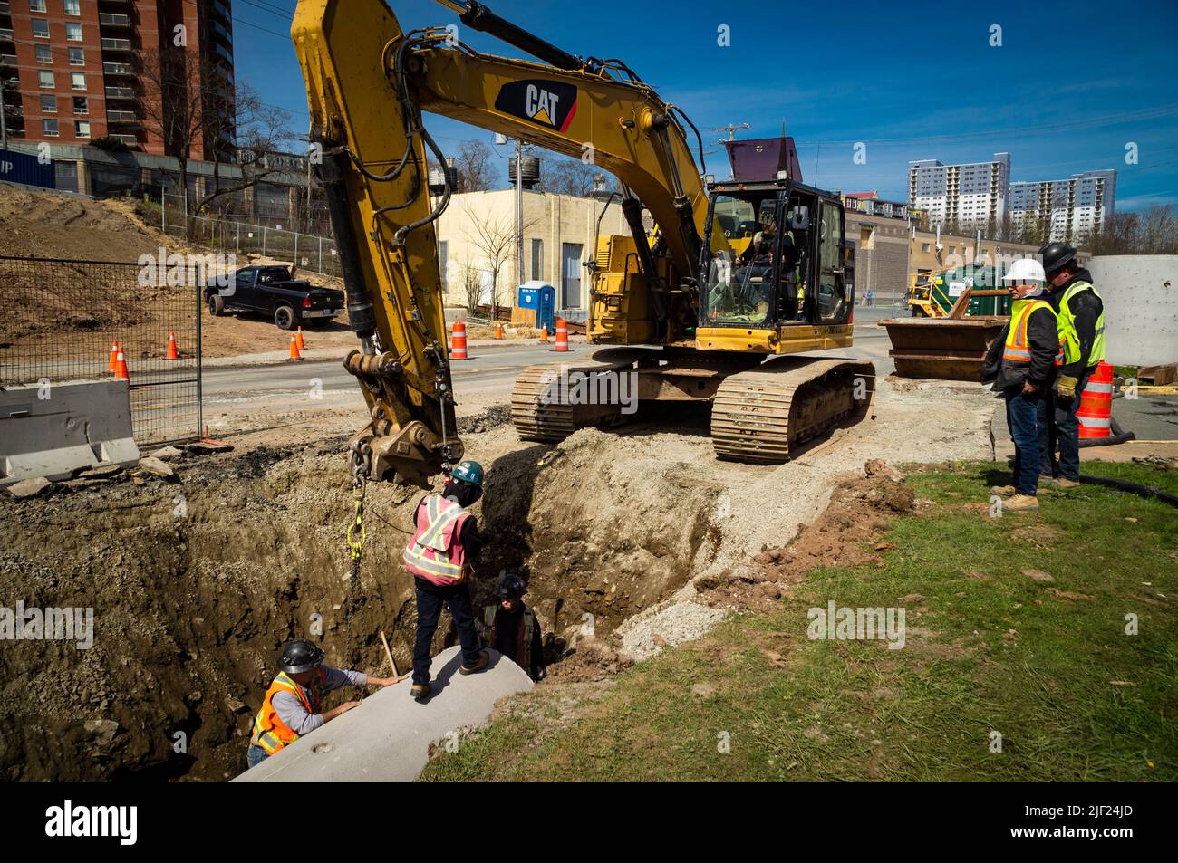 An excavator stands by after placing a section of concrete sewer pipe ...