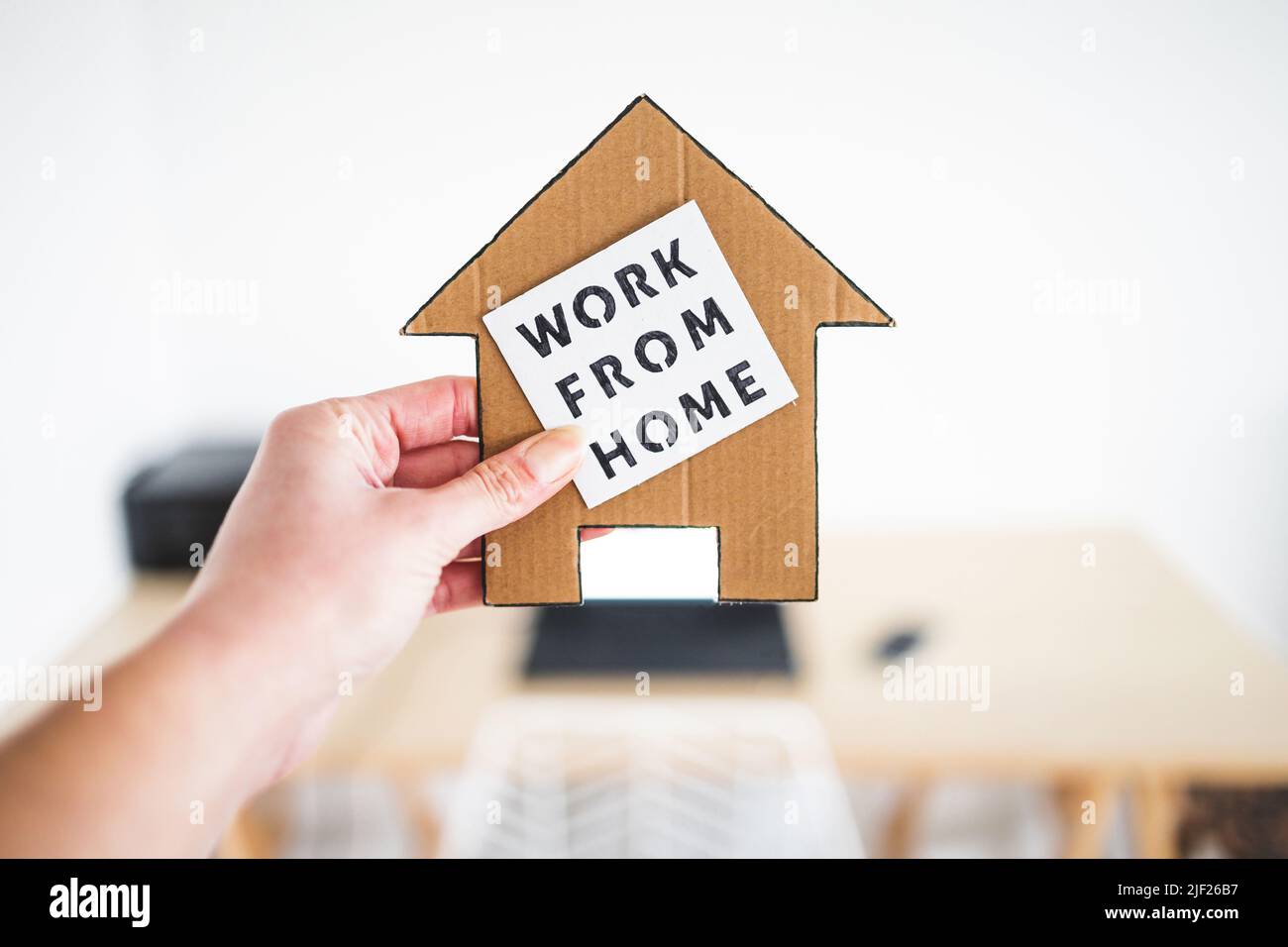 work from home sign being hold in front of out of focus home office ...