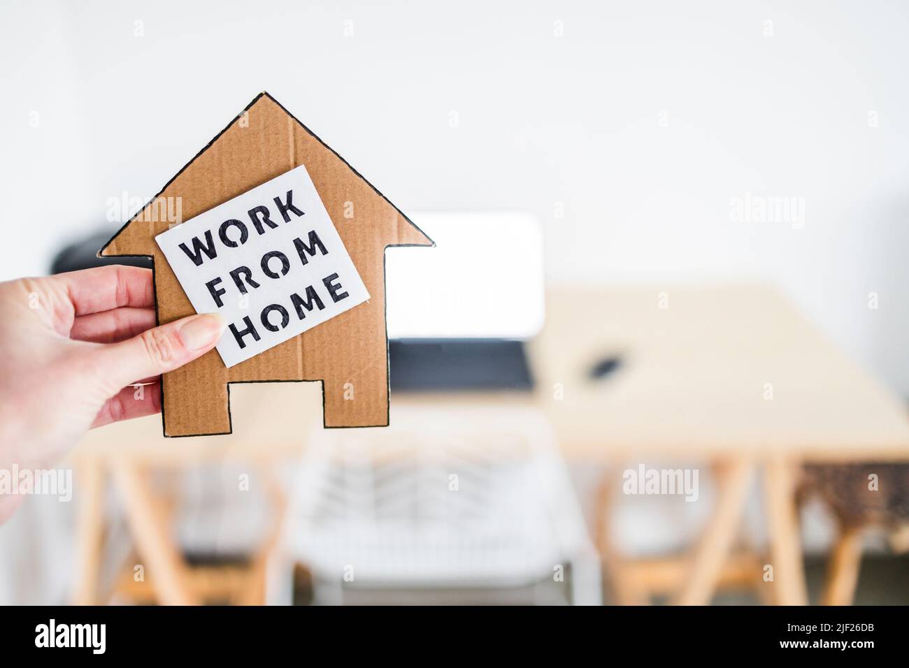 work from home sign being hold in front of out of focus home office ...