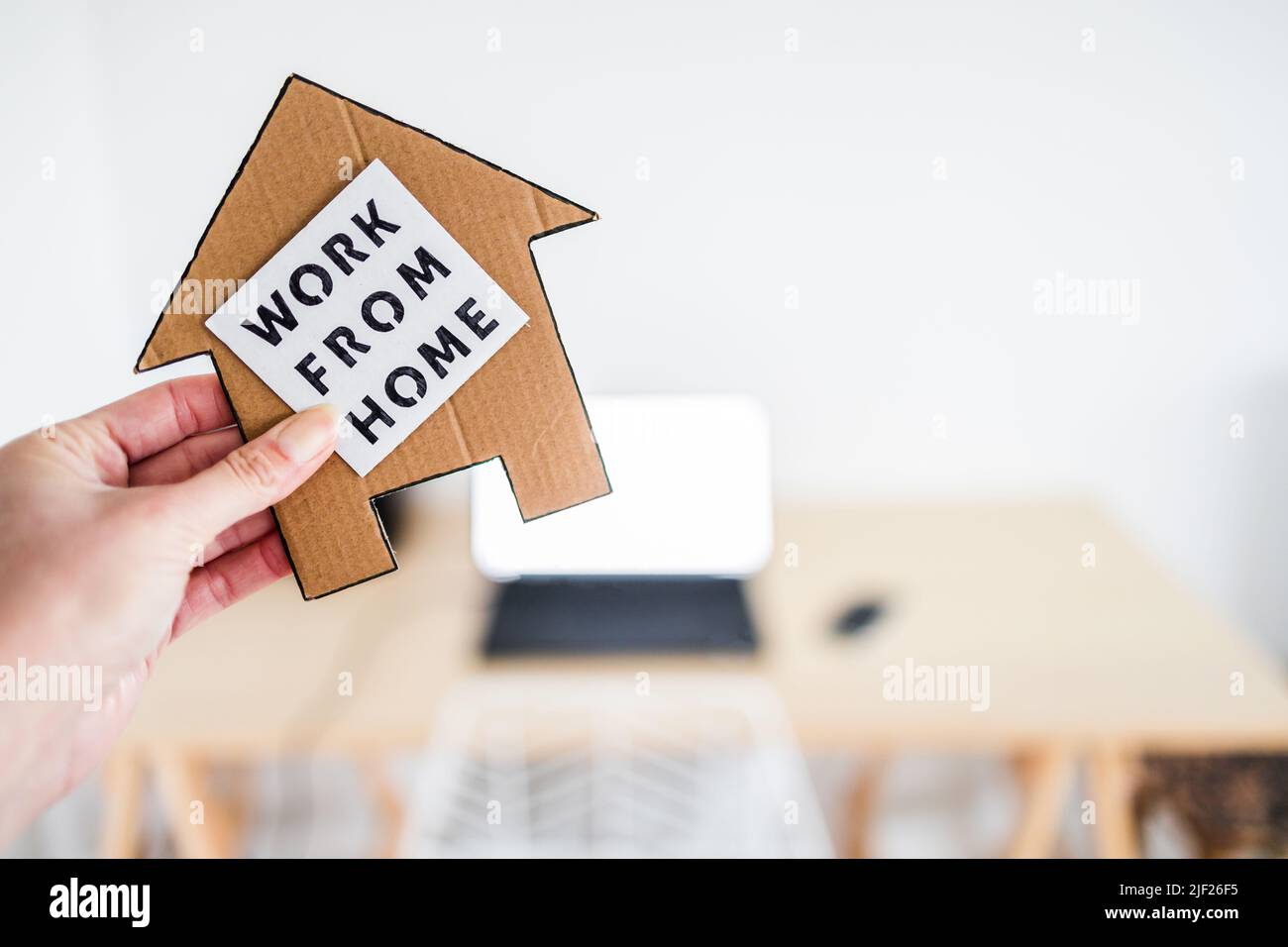 work from home sign being hold in front of out of focus home office ...