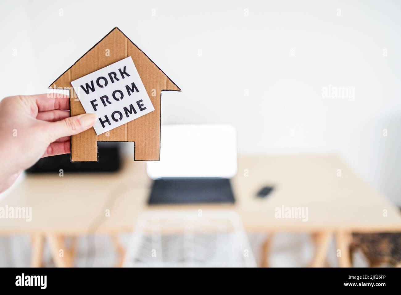 work from home sign being hold in front of out of focus home office ...