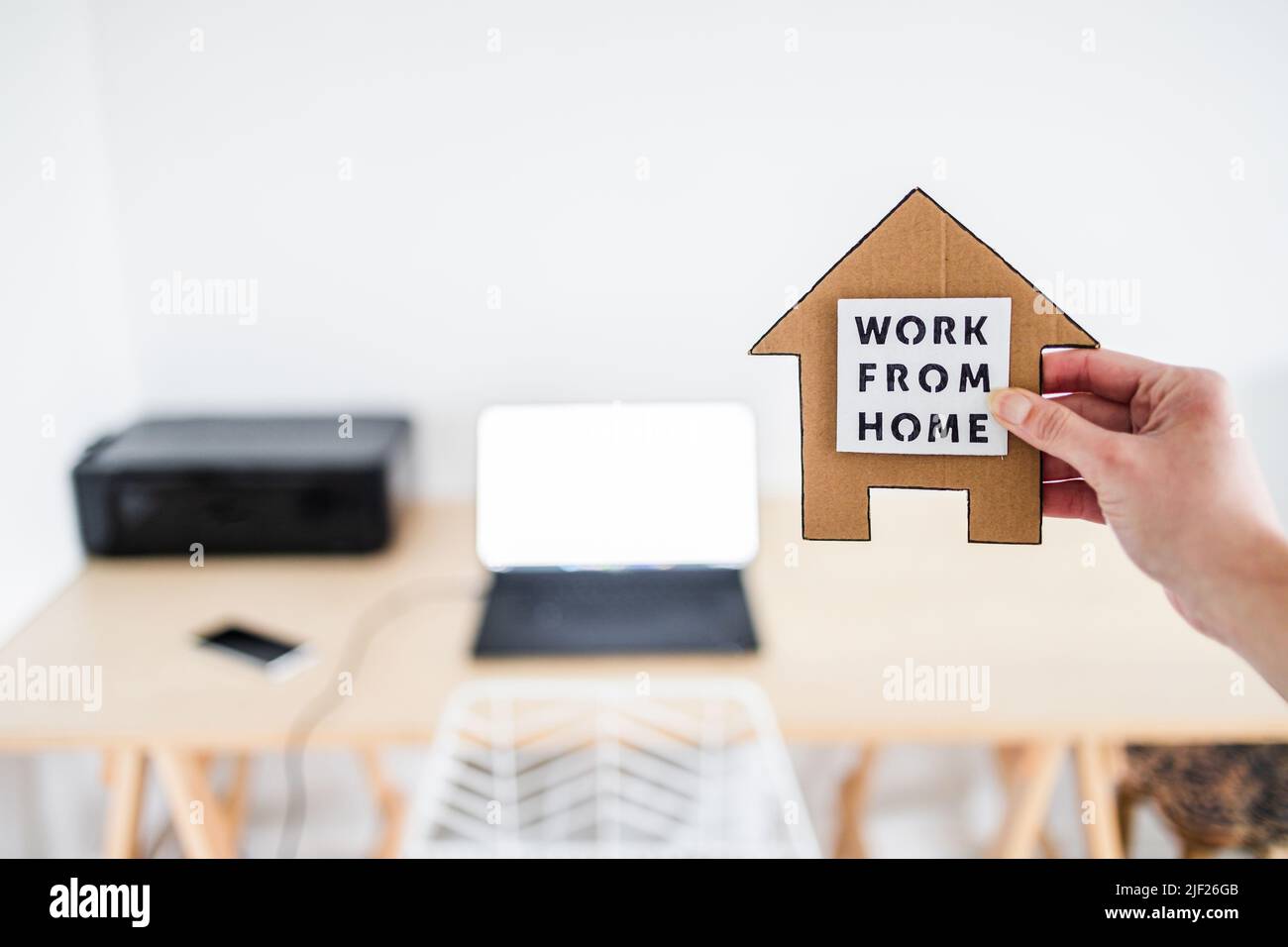 work from home sign being hold in front of out of focus home office ...