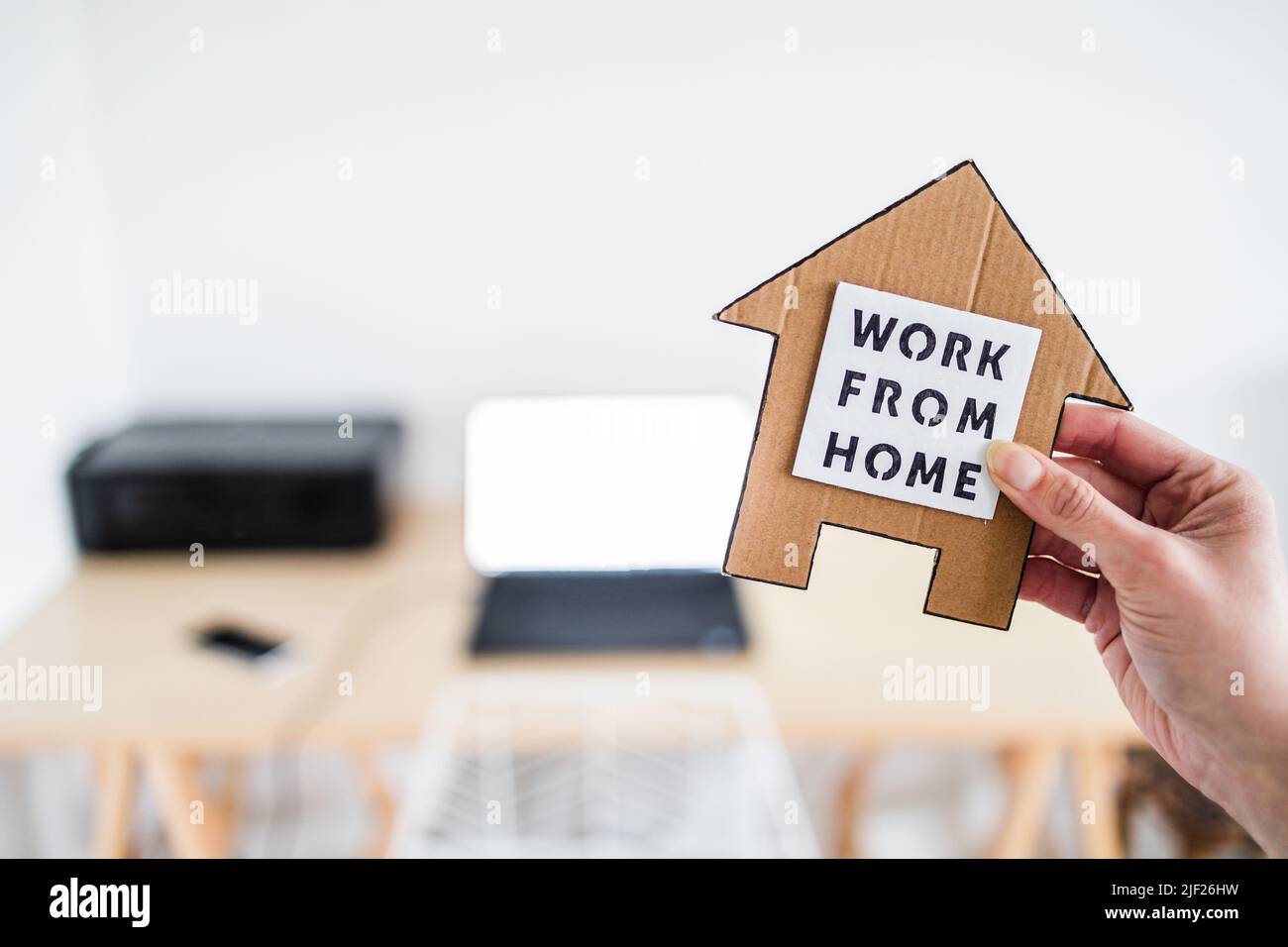 work from home sign being hold in front of out of focus home office ...