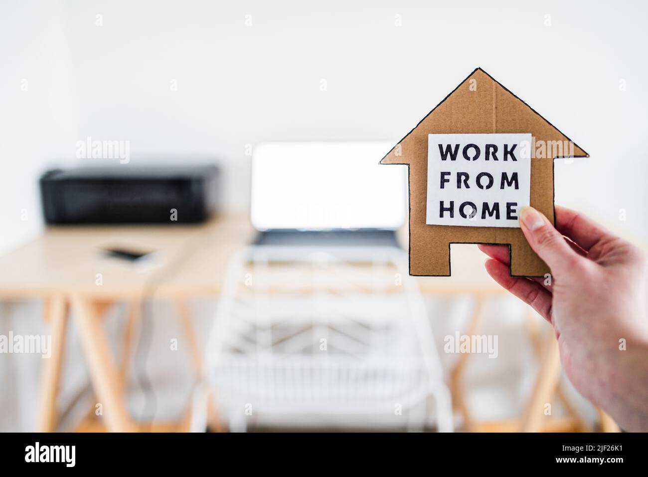 work from home sign being hold in front of out of focus home office ...
