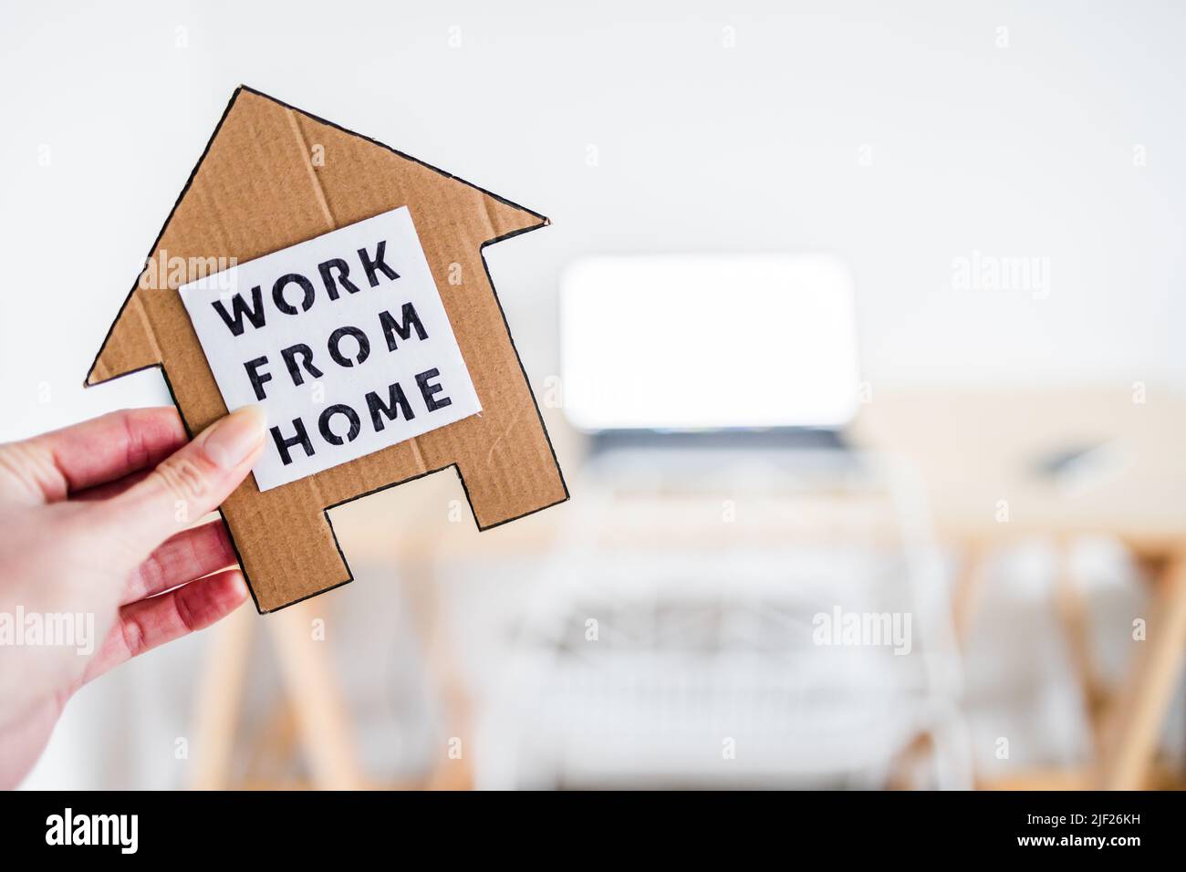 work from home sign being hold in front of out of focus home office ...