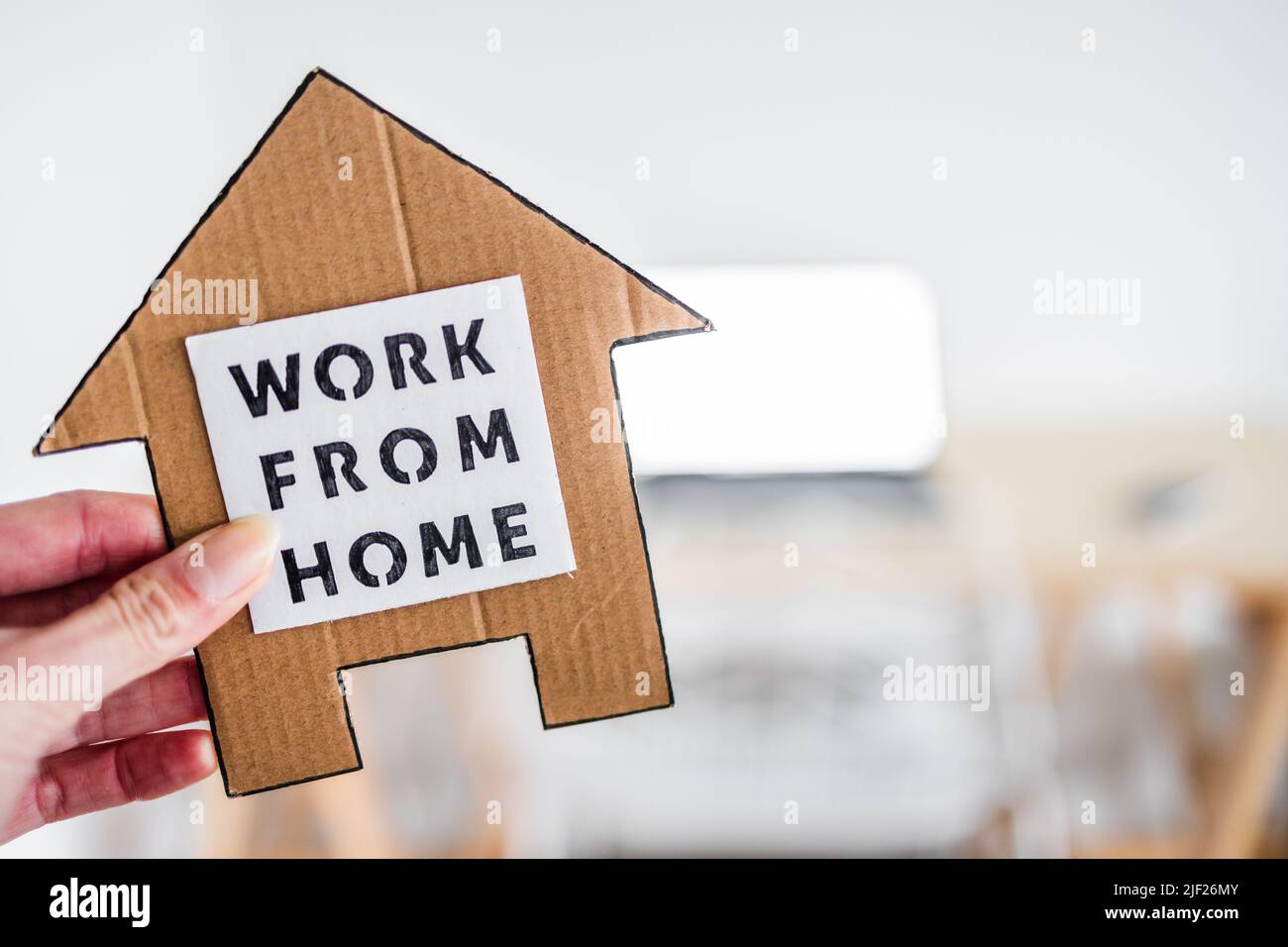 work from home sign being hold in front of out of focus home office ...