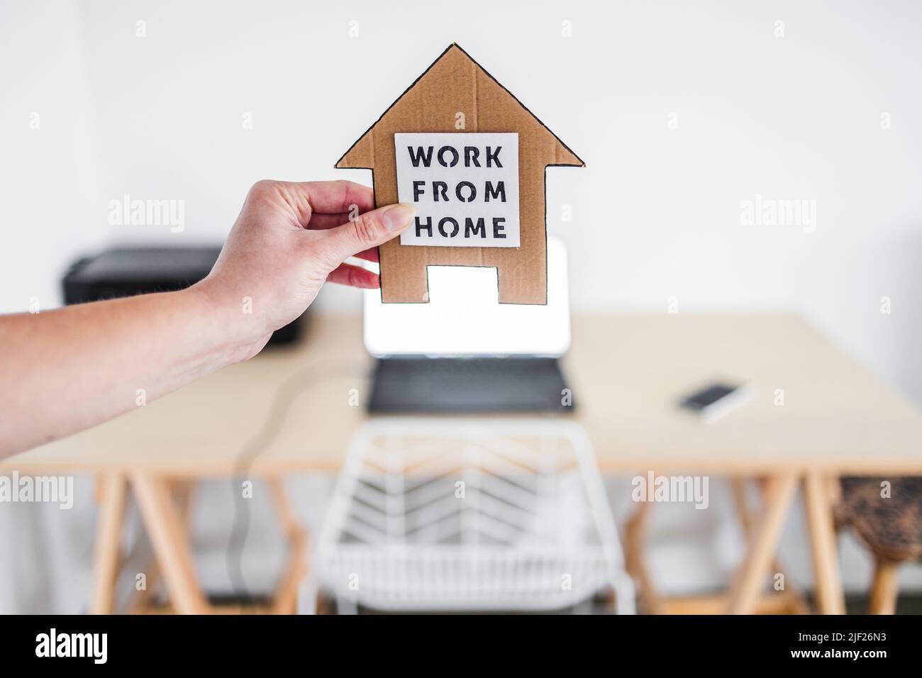 work from home sign being hold in front of out of focus home office ...
