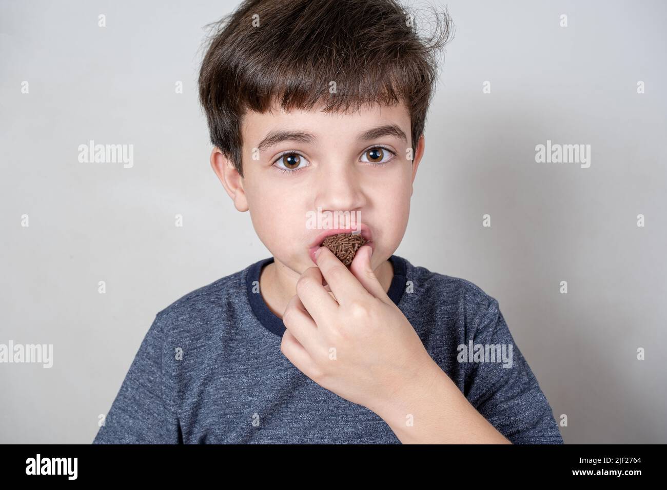9 year old kid eating a Brazilian fudge ball and facing the camera ...