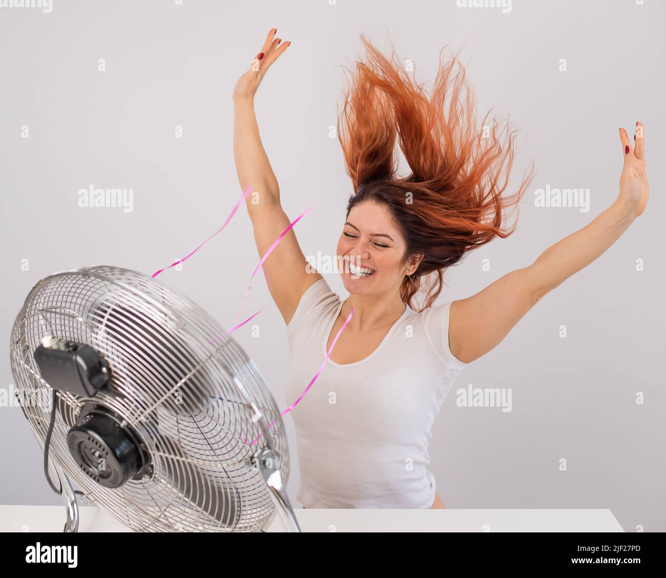 Joyful caucasian woman enjoying the wind blowing from an electric fan ...